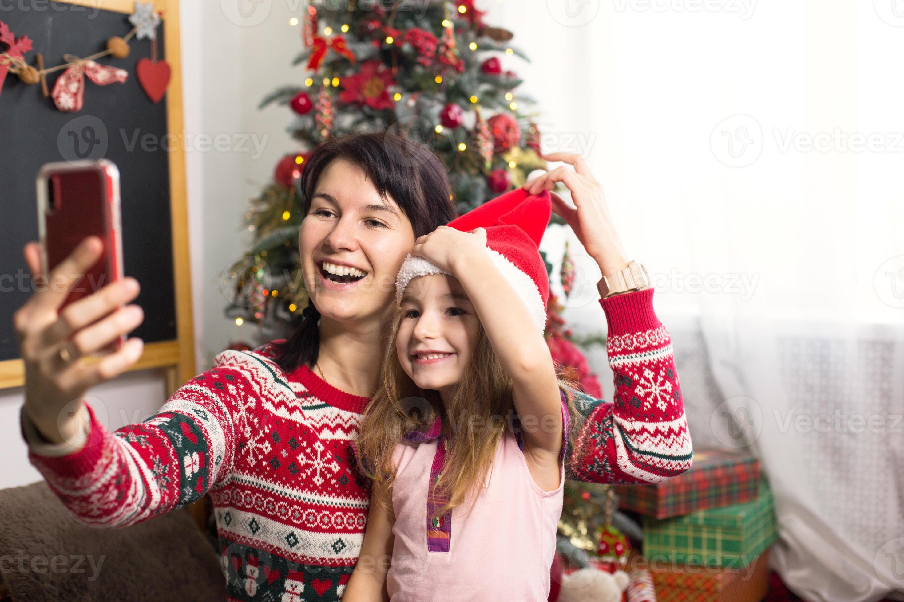 Mom And Daughter Are Sitting Near The Christmas Tree Hugging Taking