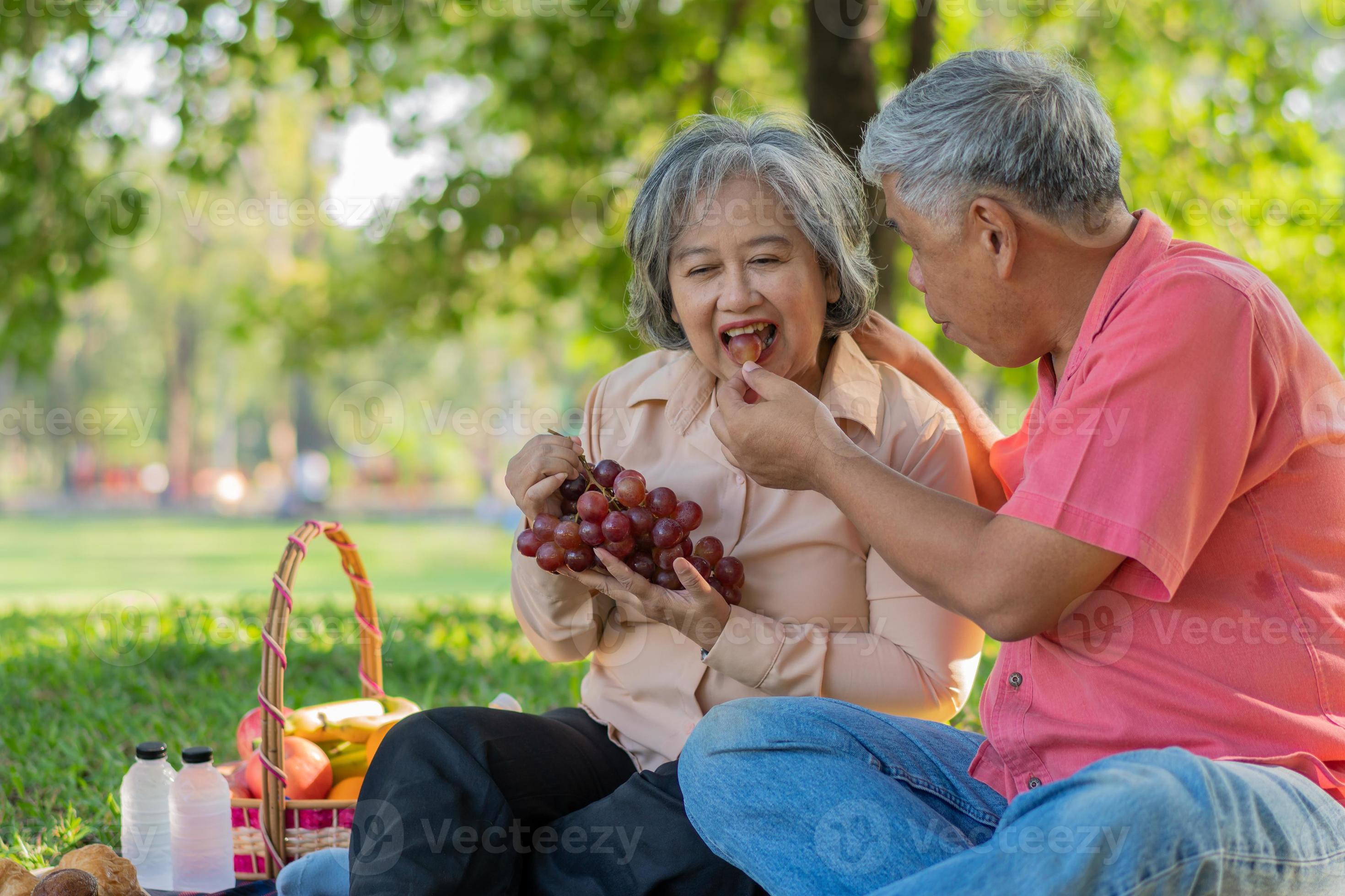 Happy old elderly couple spouses relaxing and sitting on a blanket in the park and sharing few ...