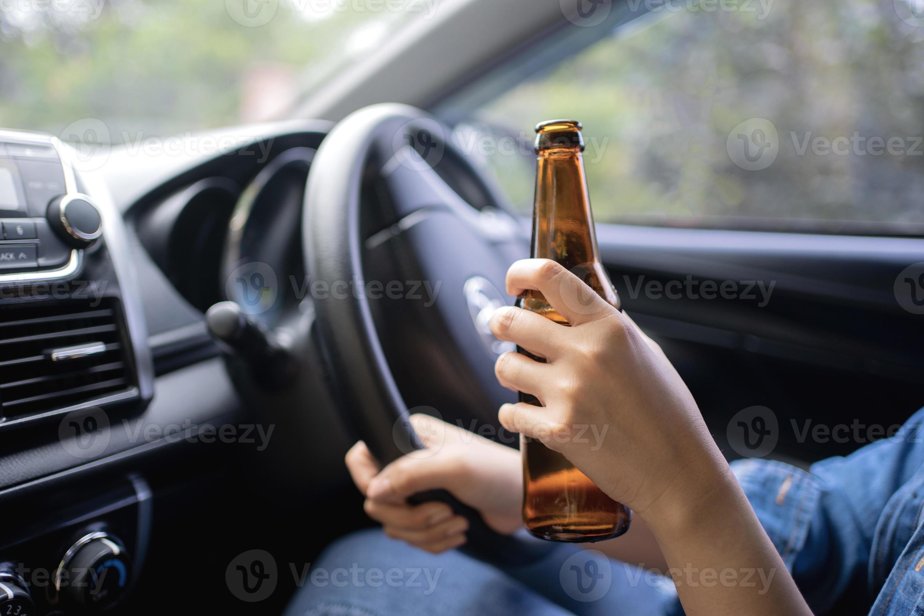 Woman drinking from a beer bottle while driving car, a concept of ...