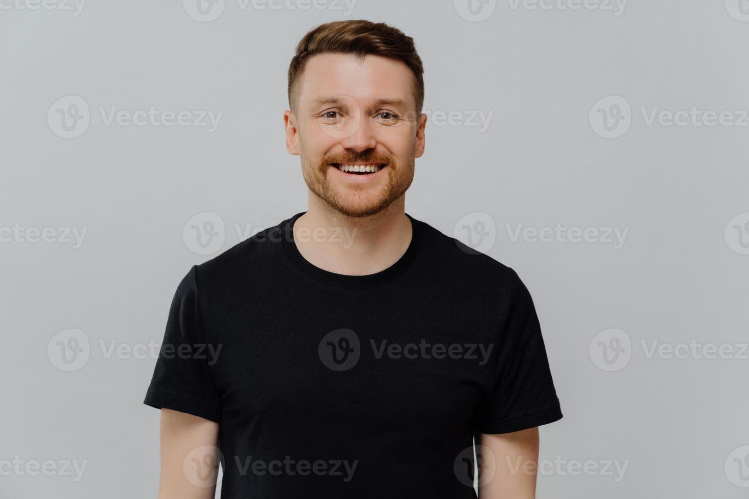 Young positive handsome man smiling at camera while posing against grey ... Young positive handsome man smiling at camera while posing against grey ...