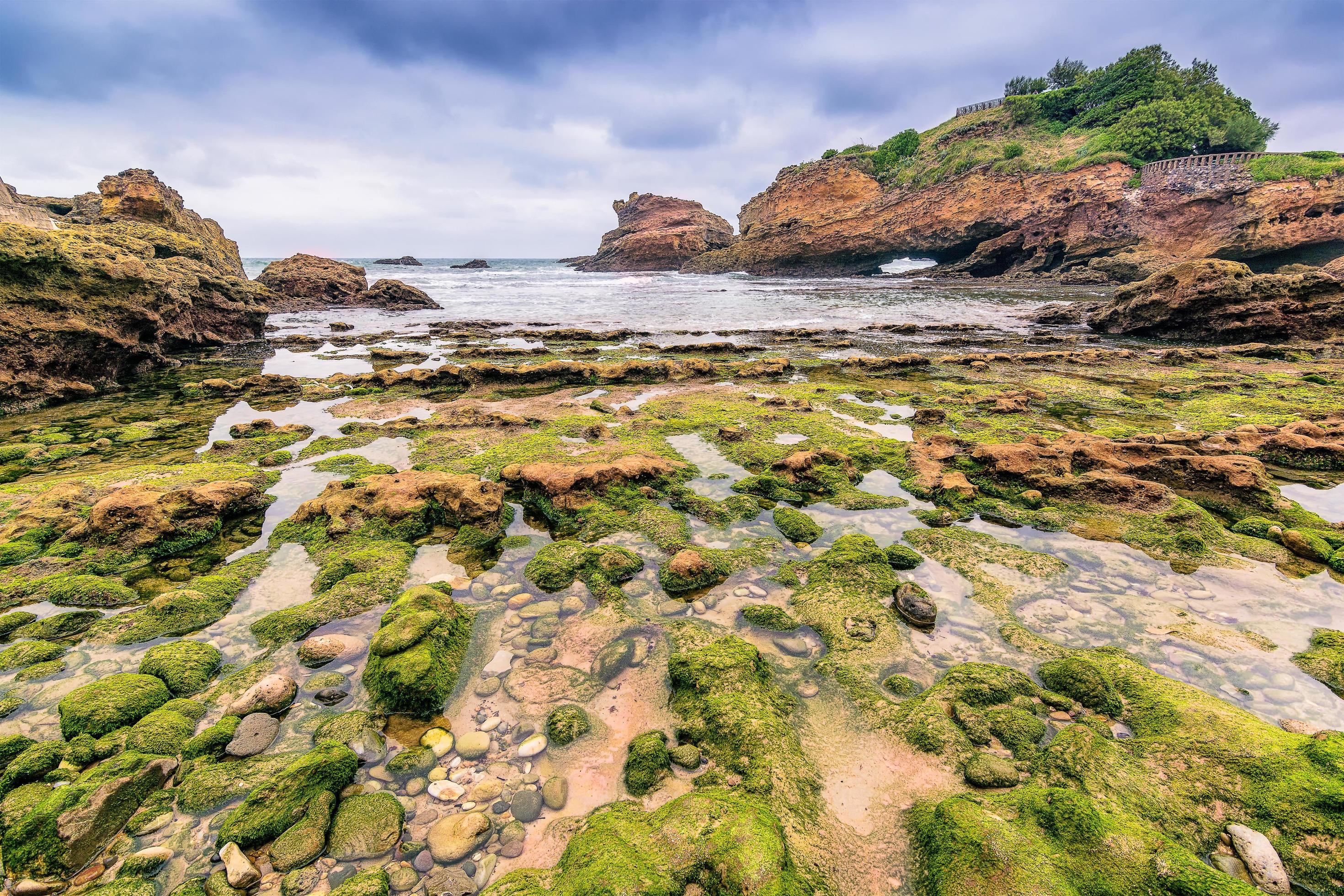 Scenic view of shoreline with rocks and shallow water at Biarritz, France against dramatic storm ...