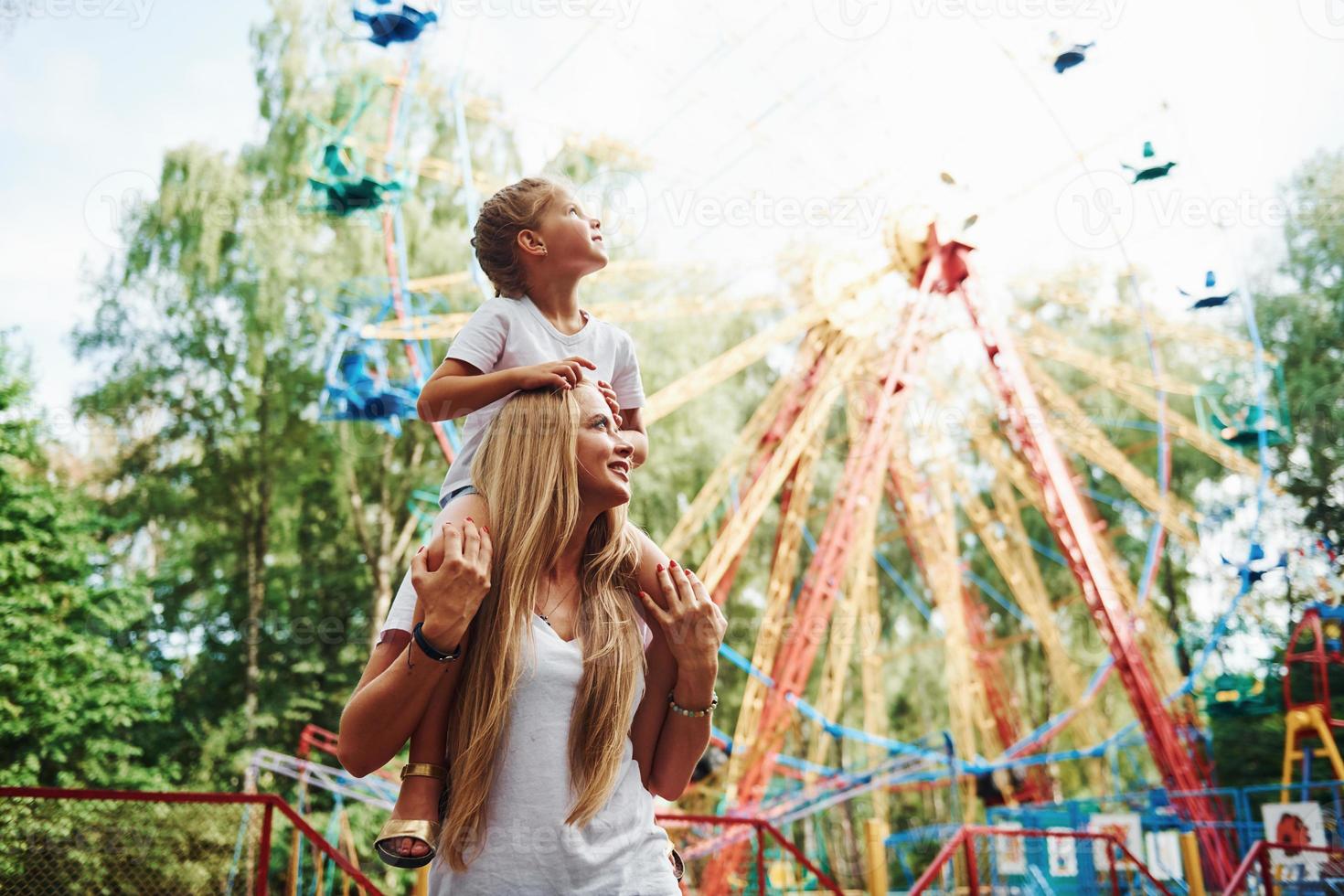 Daughter sits on the shoulders. Cheerful little girl her mother have a ... Daughter sits on the shoulders. Cheerful little girl her mother have a ...