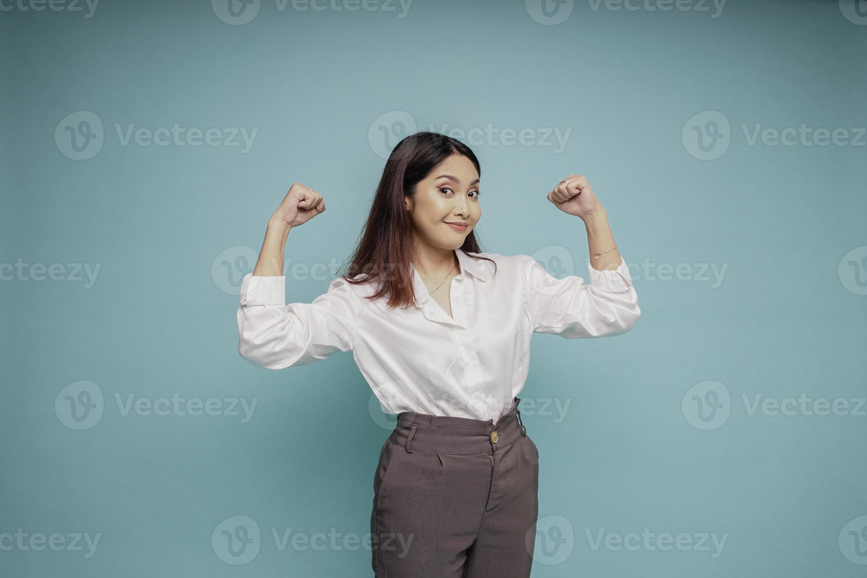 Excited Asian woman wearing a white shirt showing strong gesture by lifting her arms and muscles ...