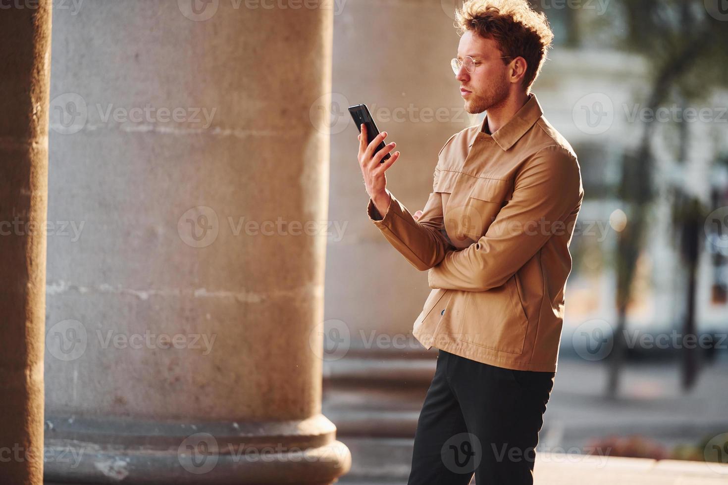 Holding phone in hand. Elegant young man in formal classy clothes outdoors in the city 15289186 ...