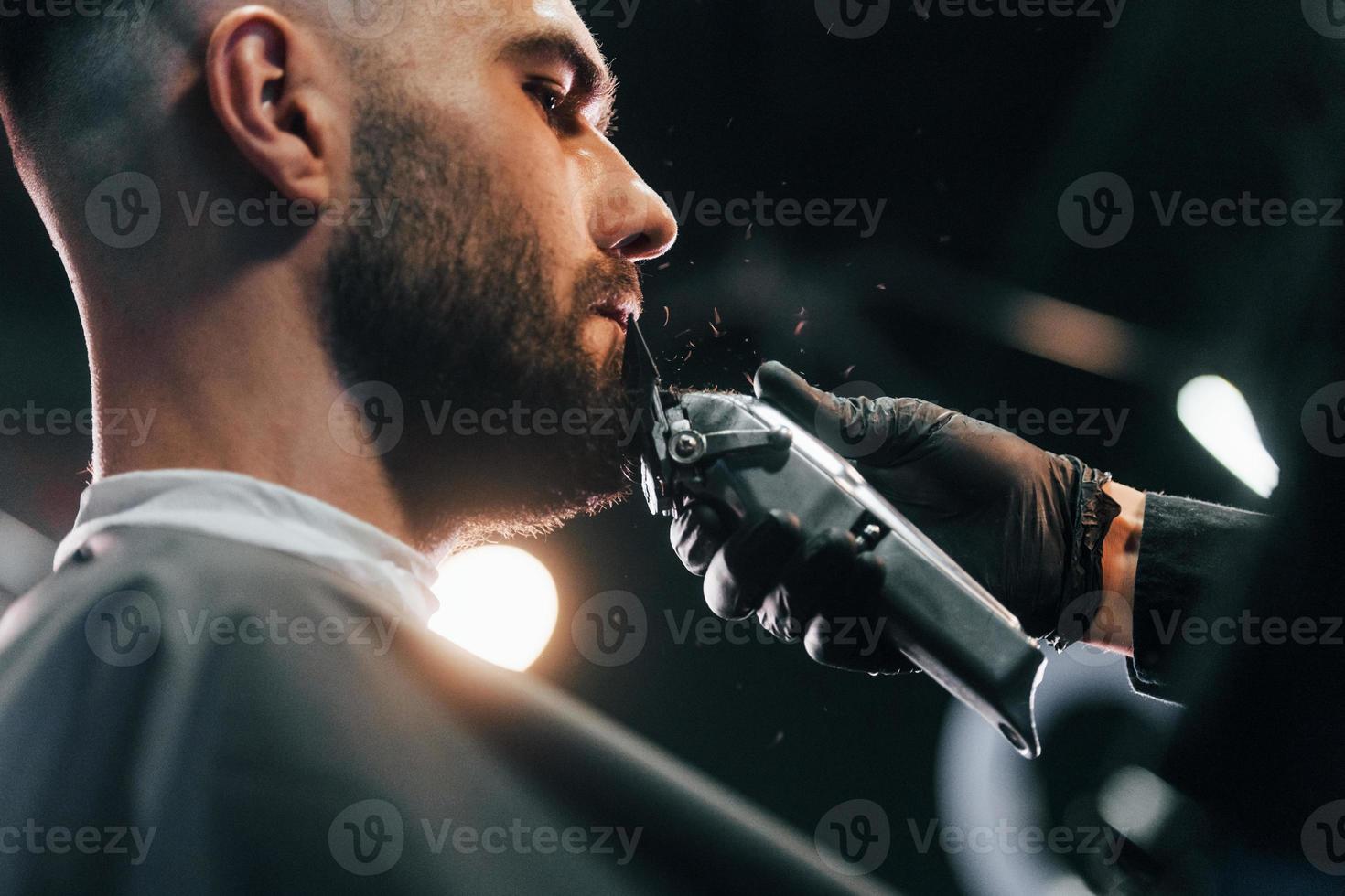 Young Man With Stylish Hairstyle Sitting And Getting His Beard Shaved