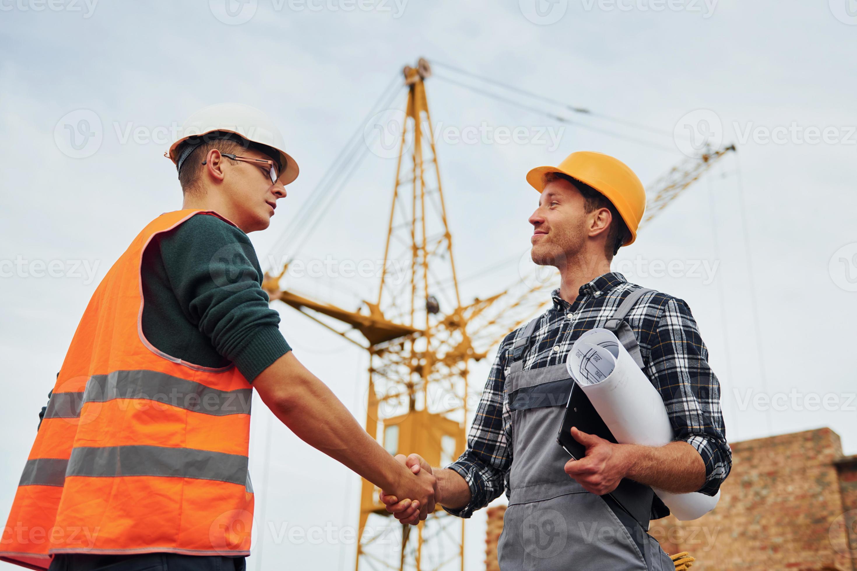 Making handshake. Two construction workers in uniform and safety ...