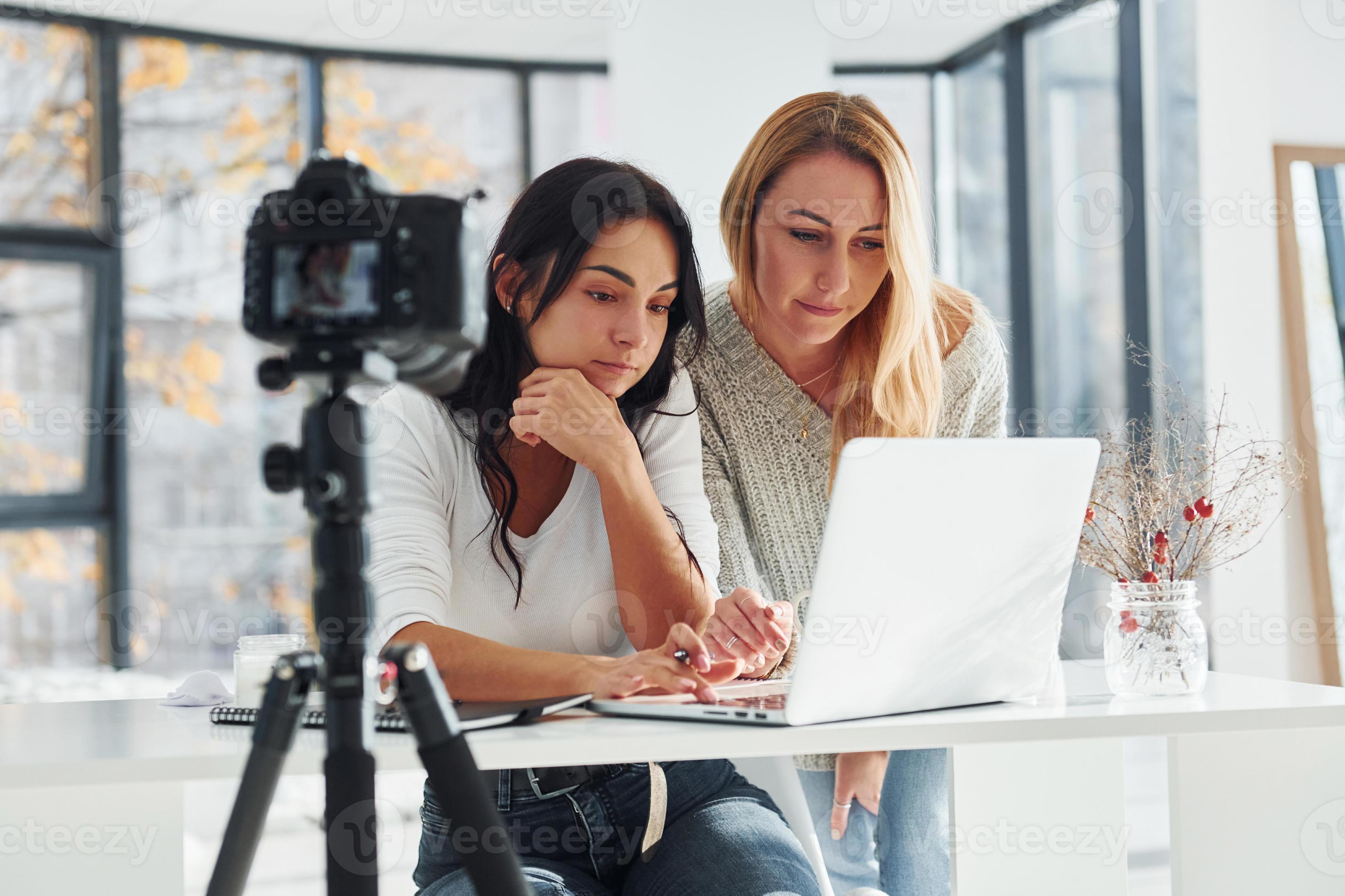 Camera on tripod is recording. Two young female freelancers working indoors in the office with ...