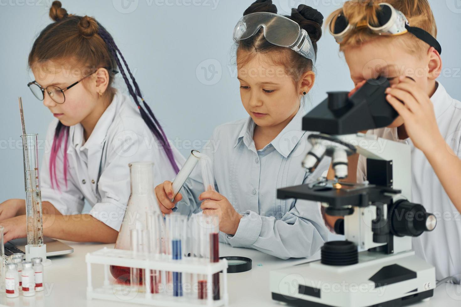 Using microscope. Children in white coats plays a scientists in lab by ... Using microscope. Children in white coats plays a scientists in lab by ...
