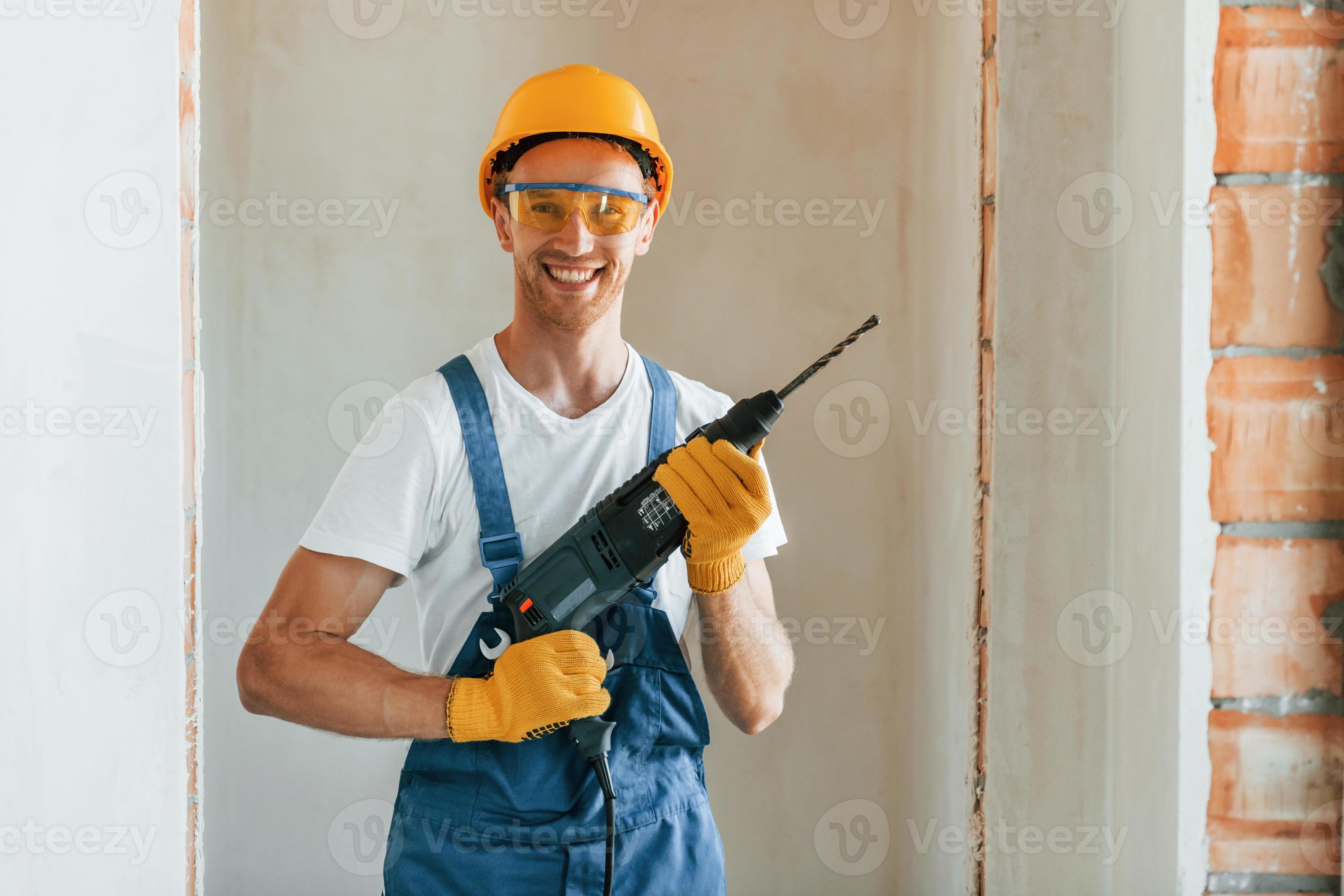Holding drill. Young man working in uniform at construction at daytime ...