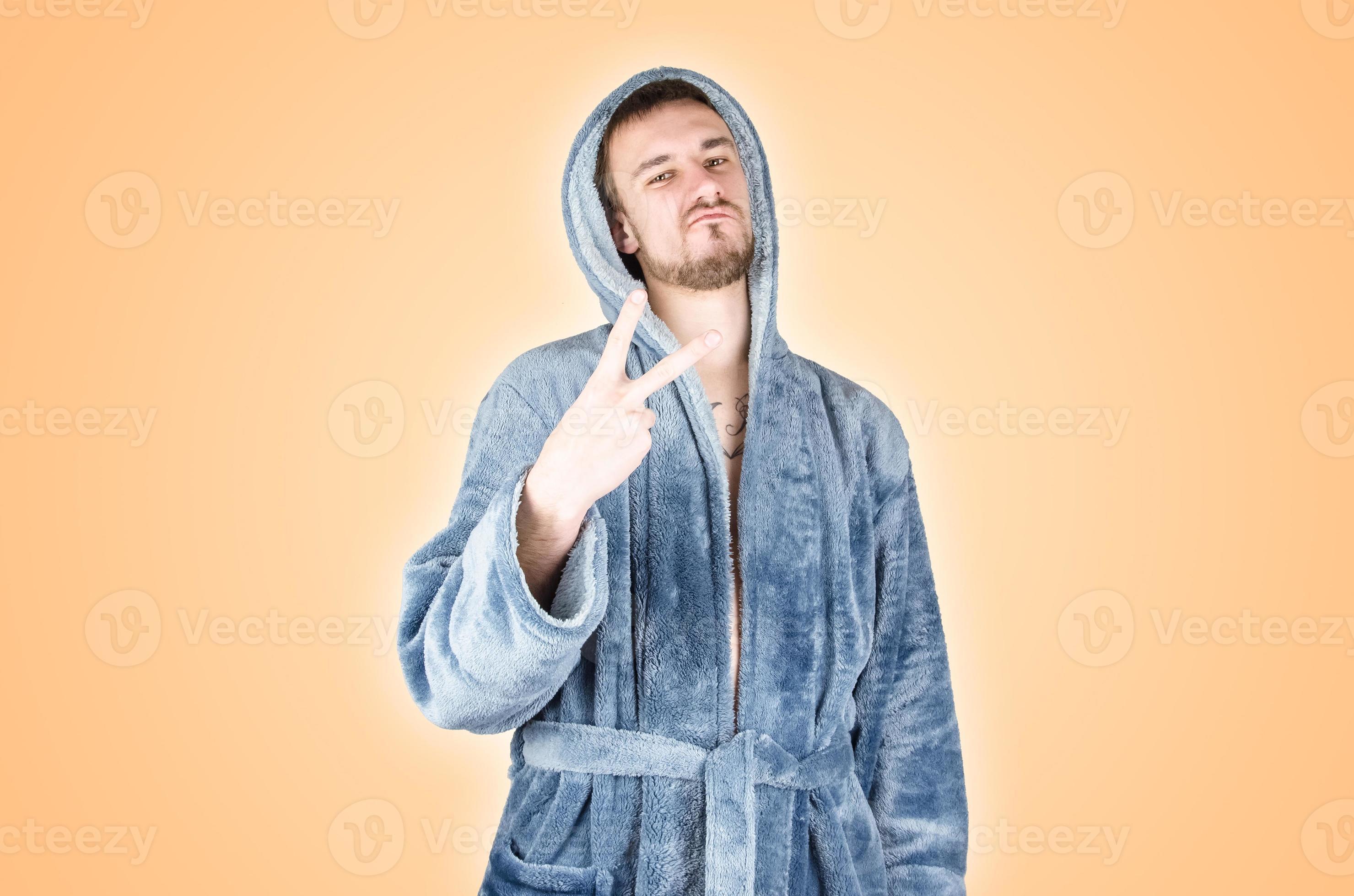 Portrait Of Young Caucasian Bearded Man In Blue Bathrobe Shows Victory