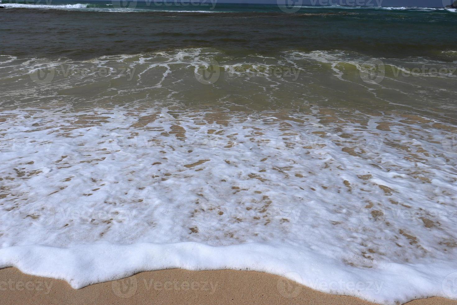 Ocean shore with sandy beach and advancing wave. Water foam with smooth ...