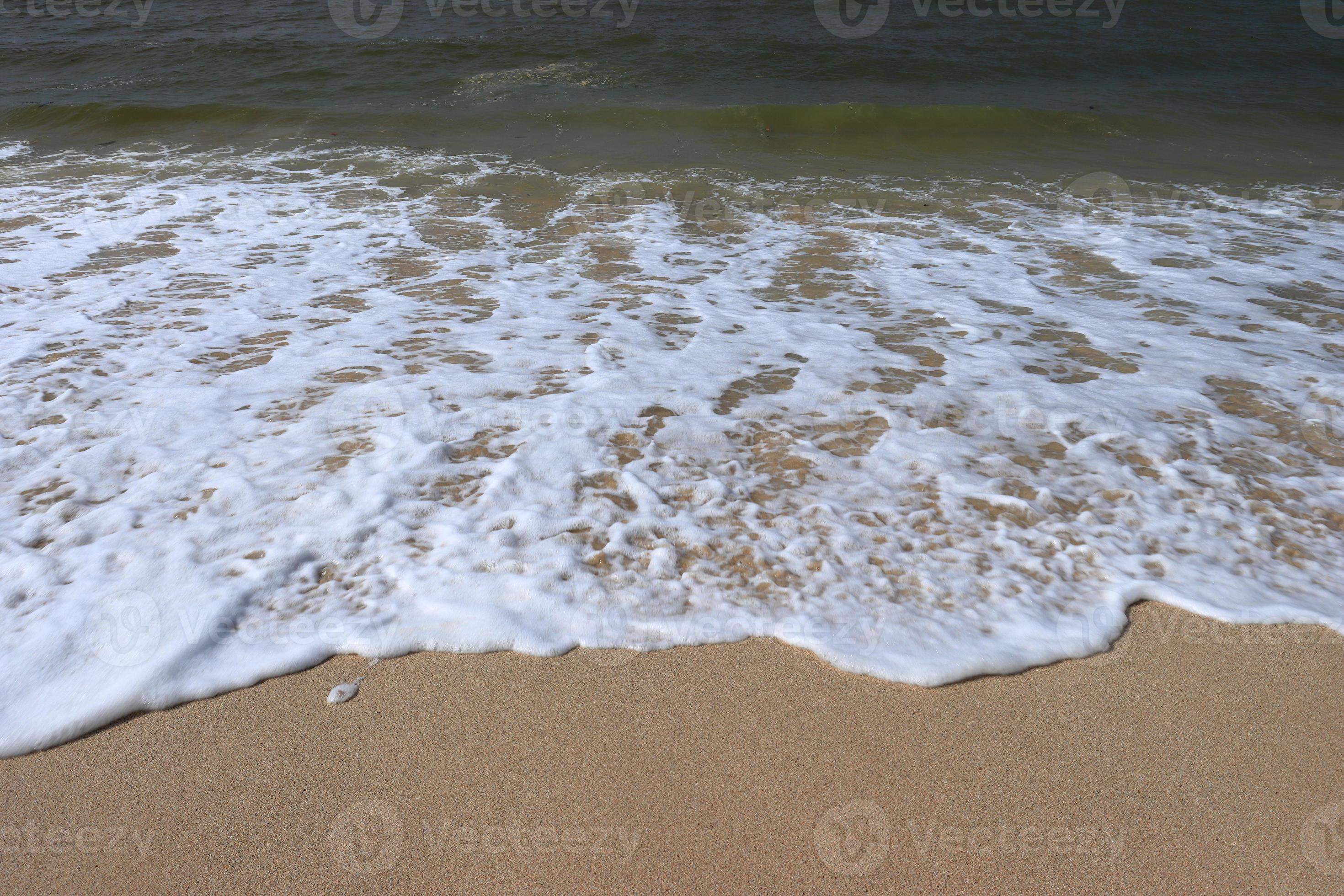 Ocean shore with sandy beach and advancing wave. Water foam with smooth ...