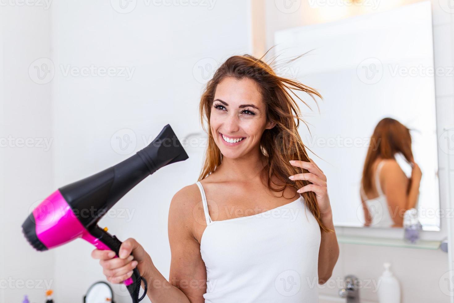 Cute woman in bathroom blow drying her hair in the morning. Young woman blow drying hair in ...