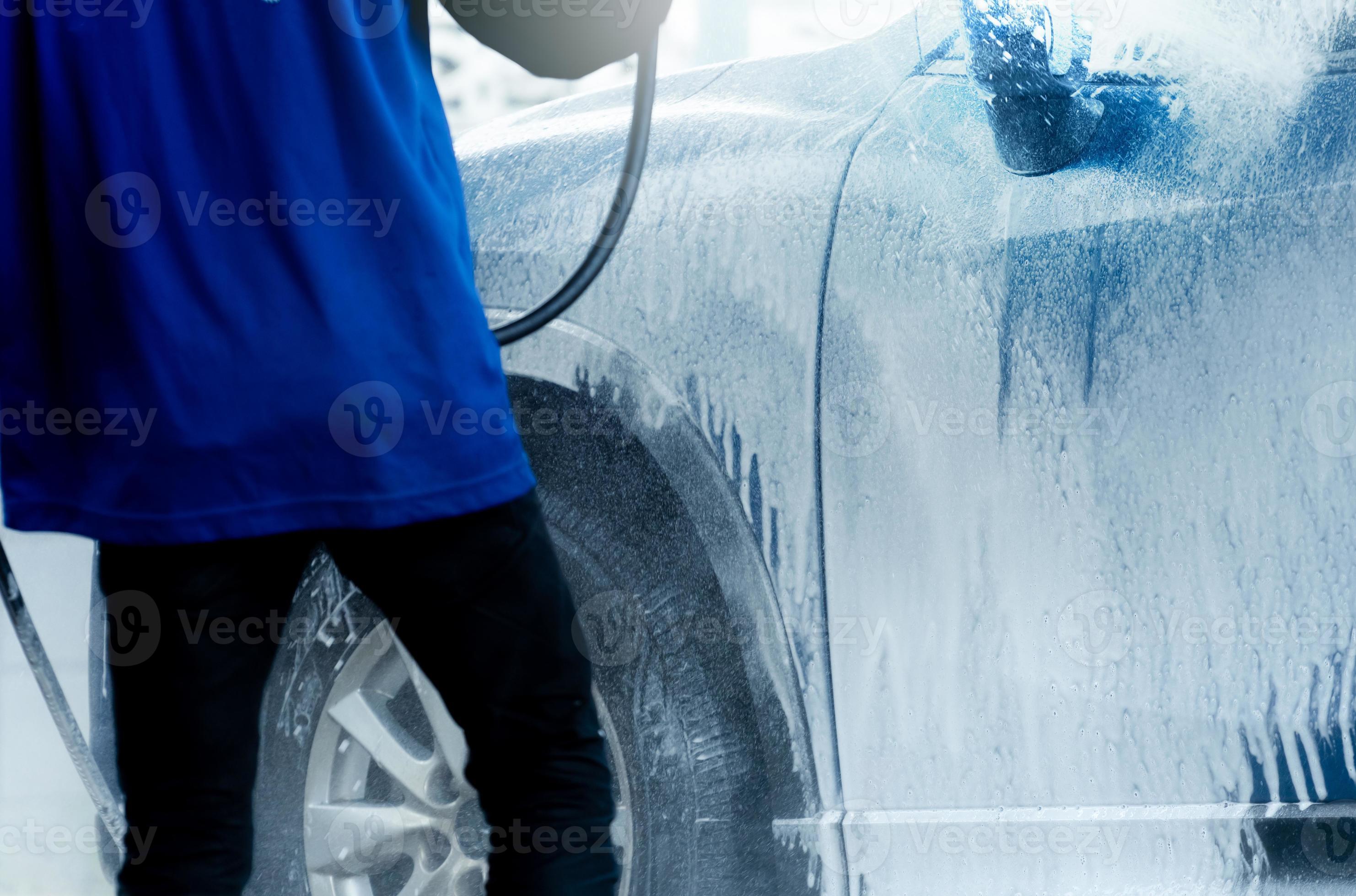Worker washes blue SUV car with soap foam. Exterior carwash. Car care business. Vehicle cleaning ...