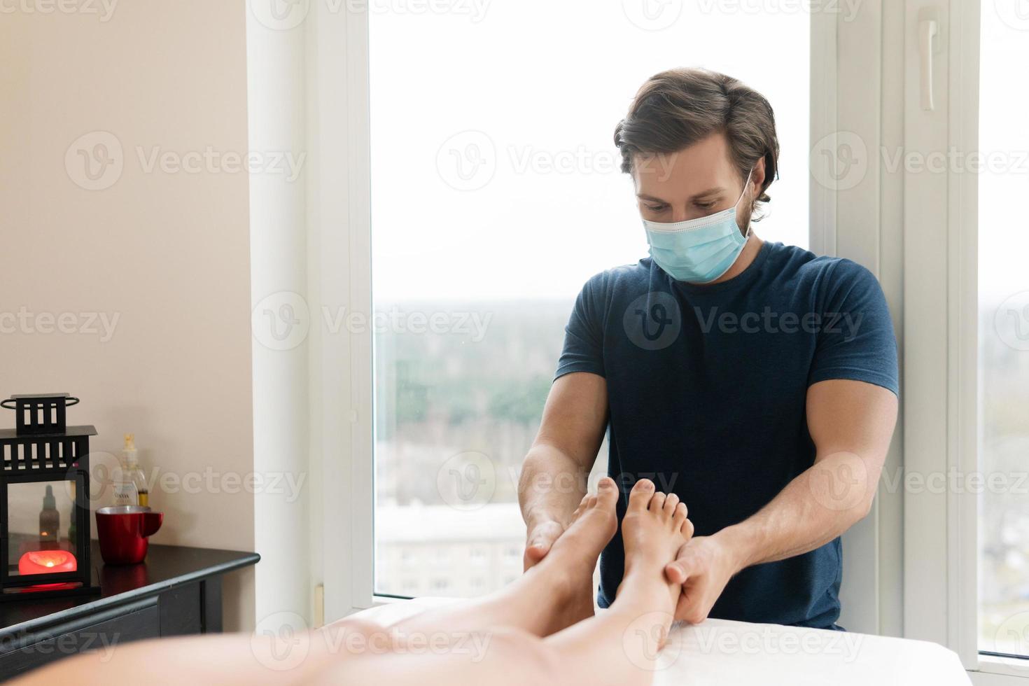 Professional Man Masseur Wearing Prevention Mask During Female Foot