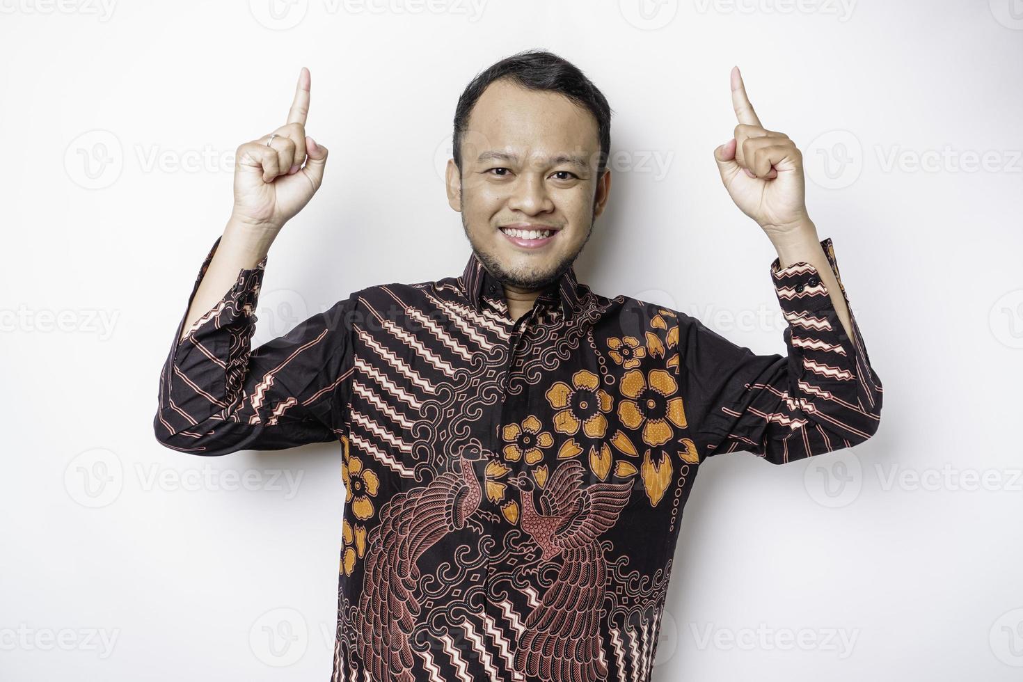 Excited Asian man wearing batik shirt pointing at the copy space on top ...