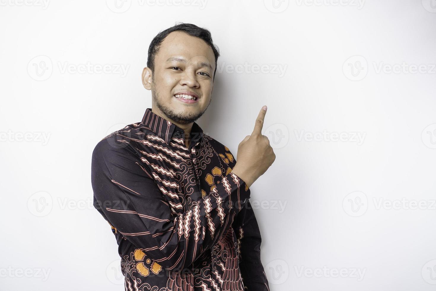 Excited Asian man wearing batik shirt pointing at the copy space on top ...