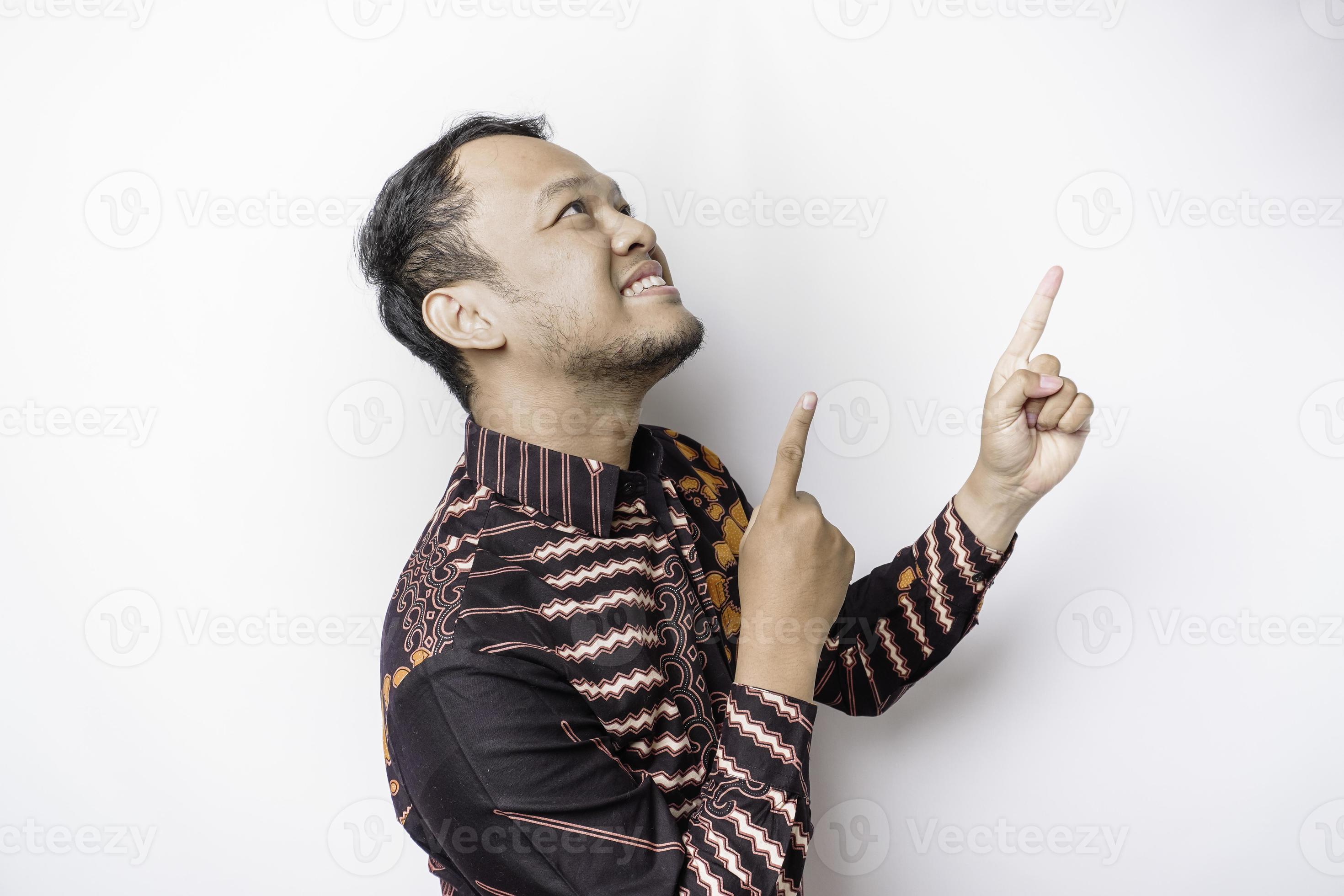 Excited Asian man wearing batik shirt pointing at the copy space on top ...