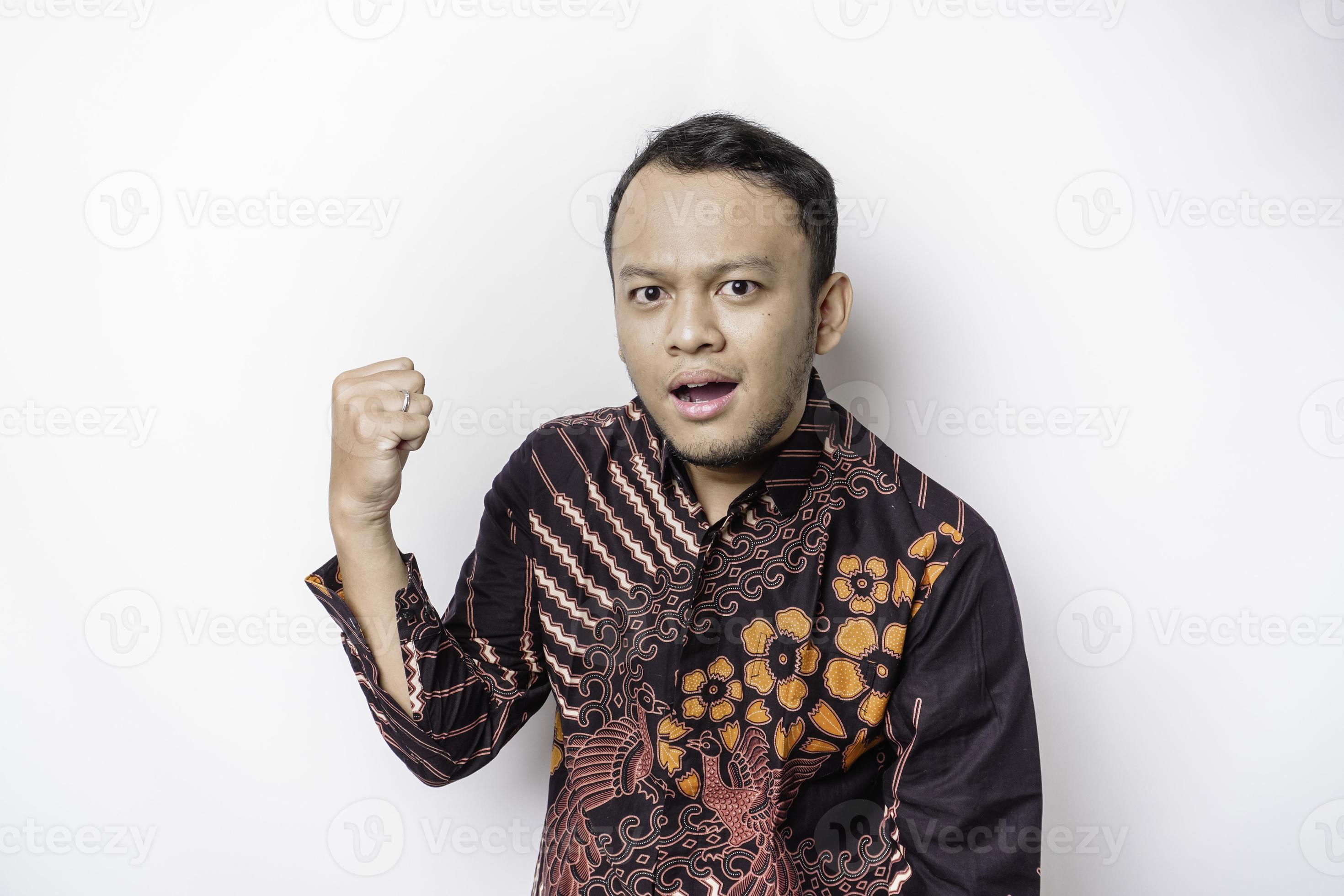 Shocked Asian man wearing batik shirt pointing at the copy space beside ...