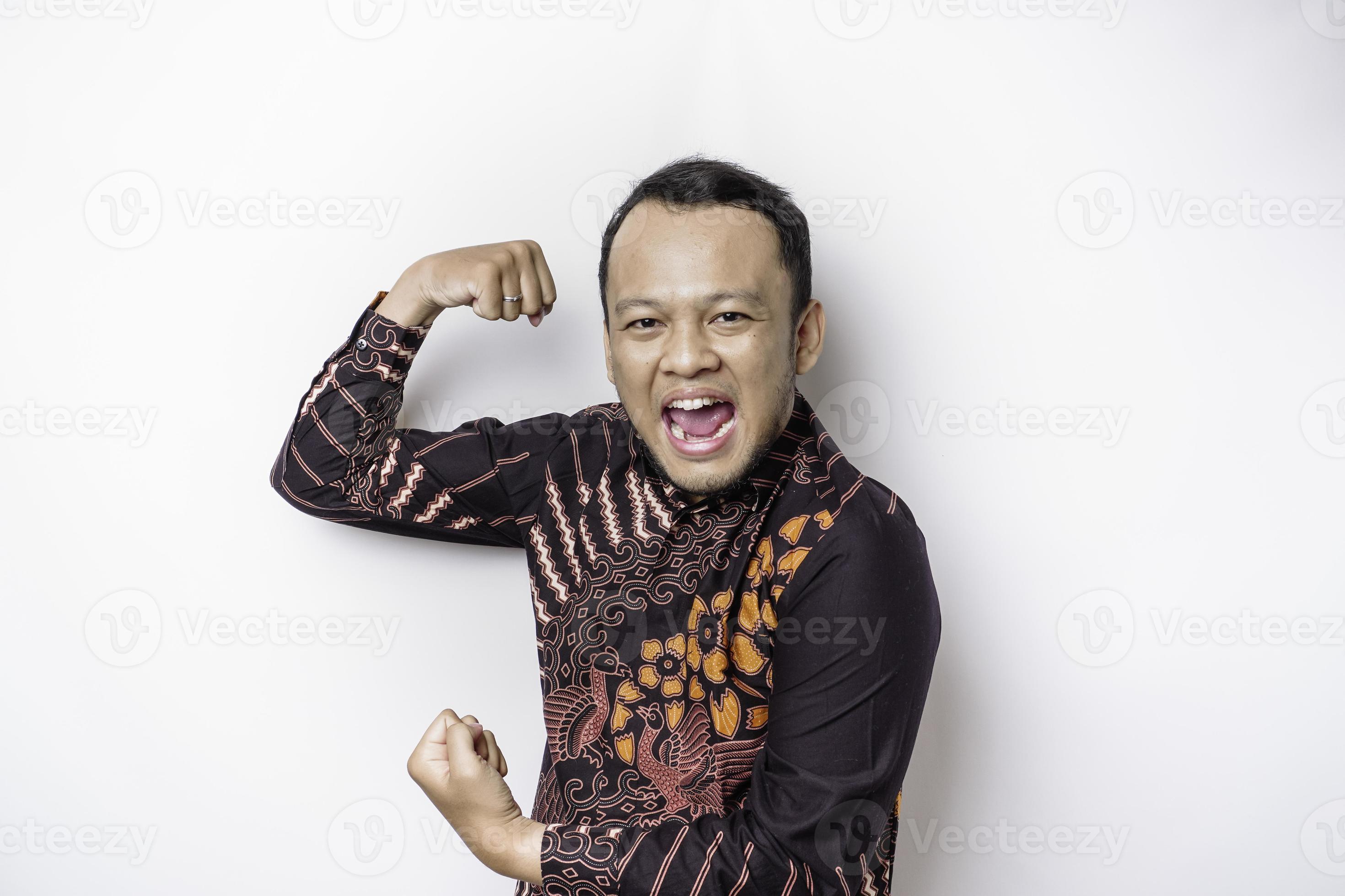 Excited Asian man wearing batik shirt showing strong gesture by lifting ...