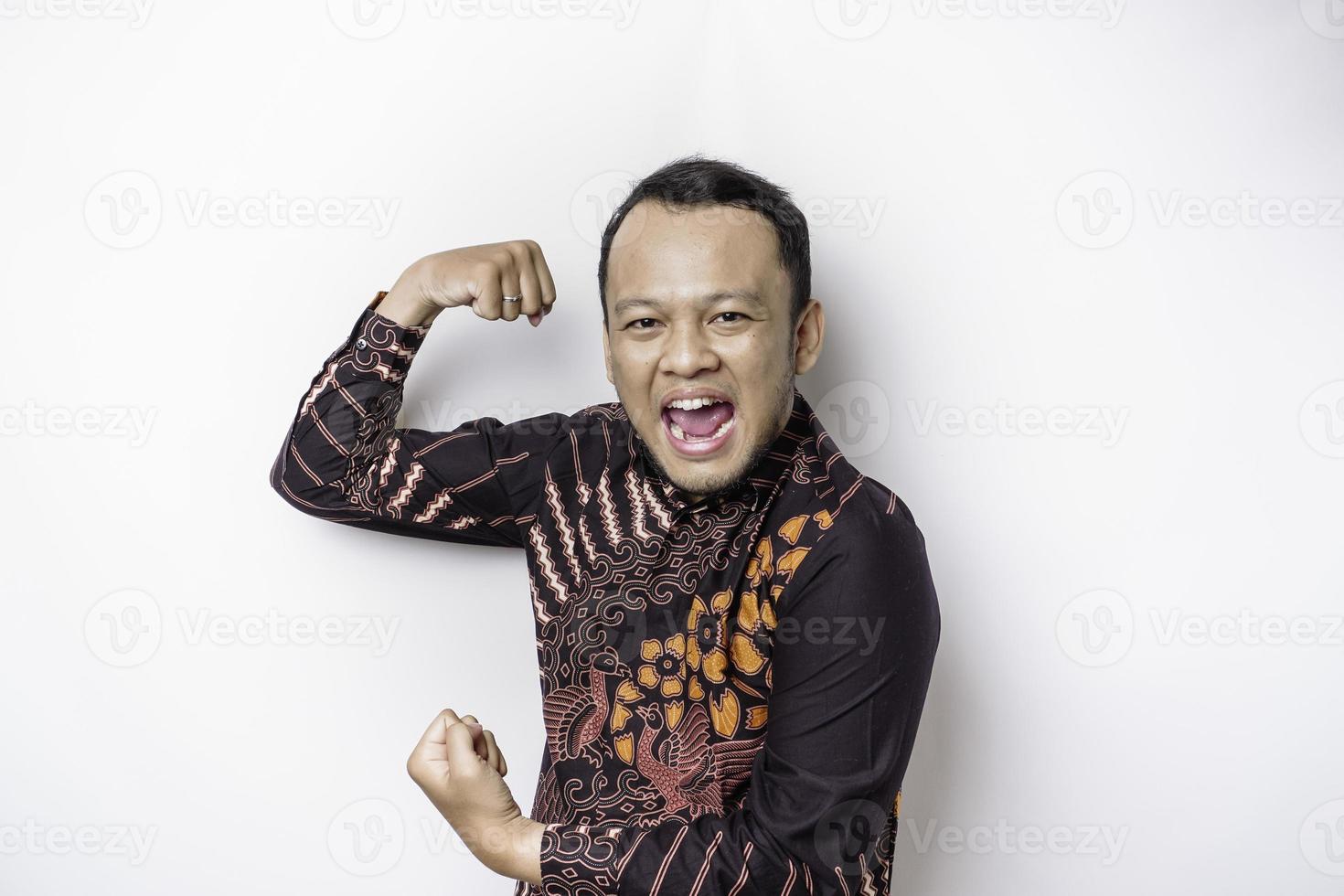 Excited Asian man wearing batik shirt showing strong gesture by lifting ...