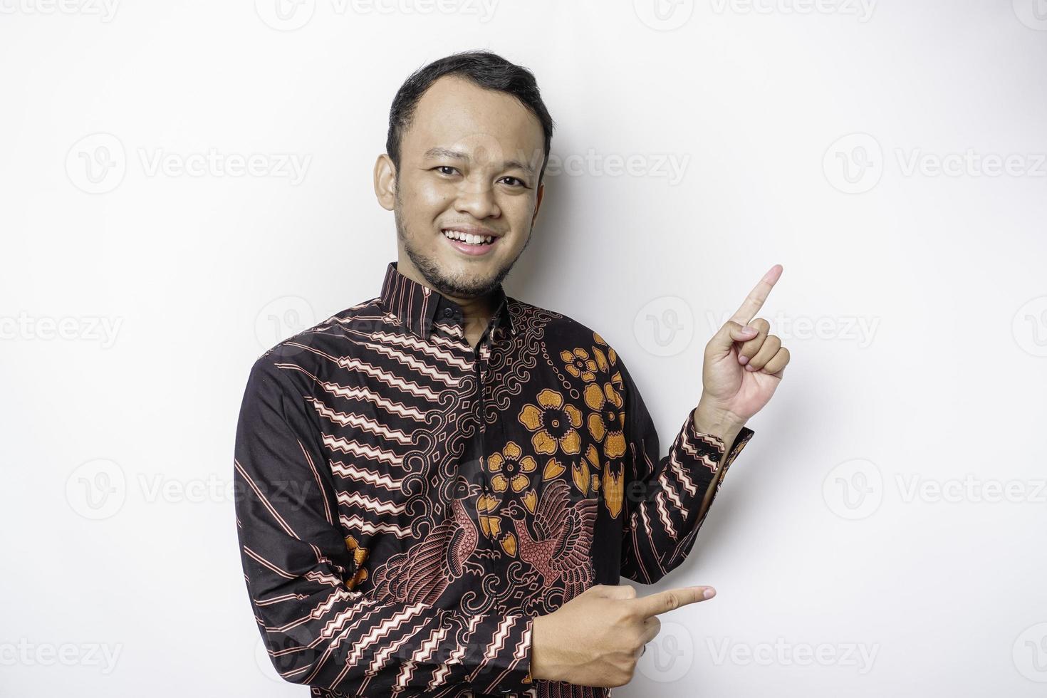 Excited Asian man wearing batik shirt pointing at the copy space beside ...