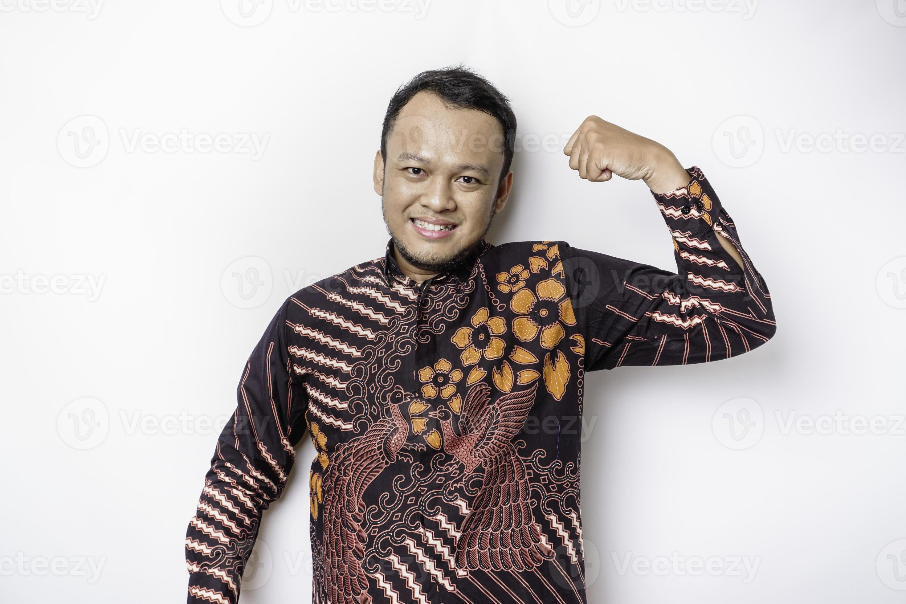 Excited Asian man wearing batik shirt showing strong gesture by lifting ...