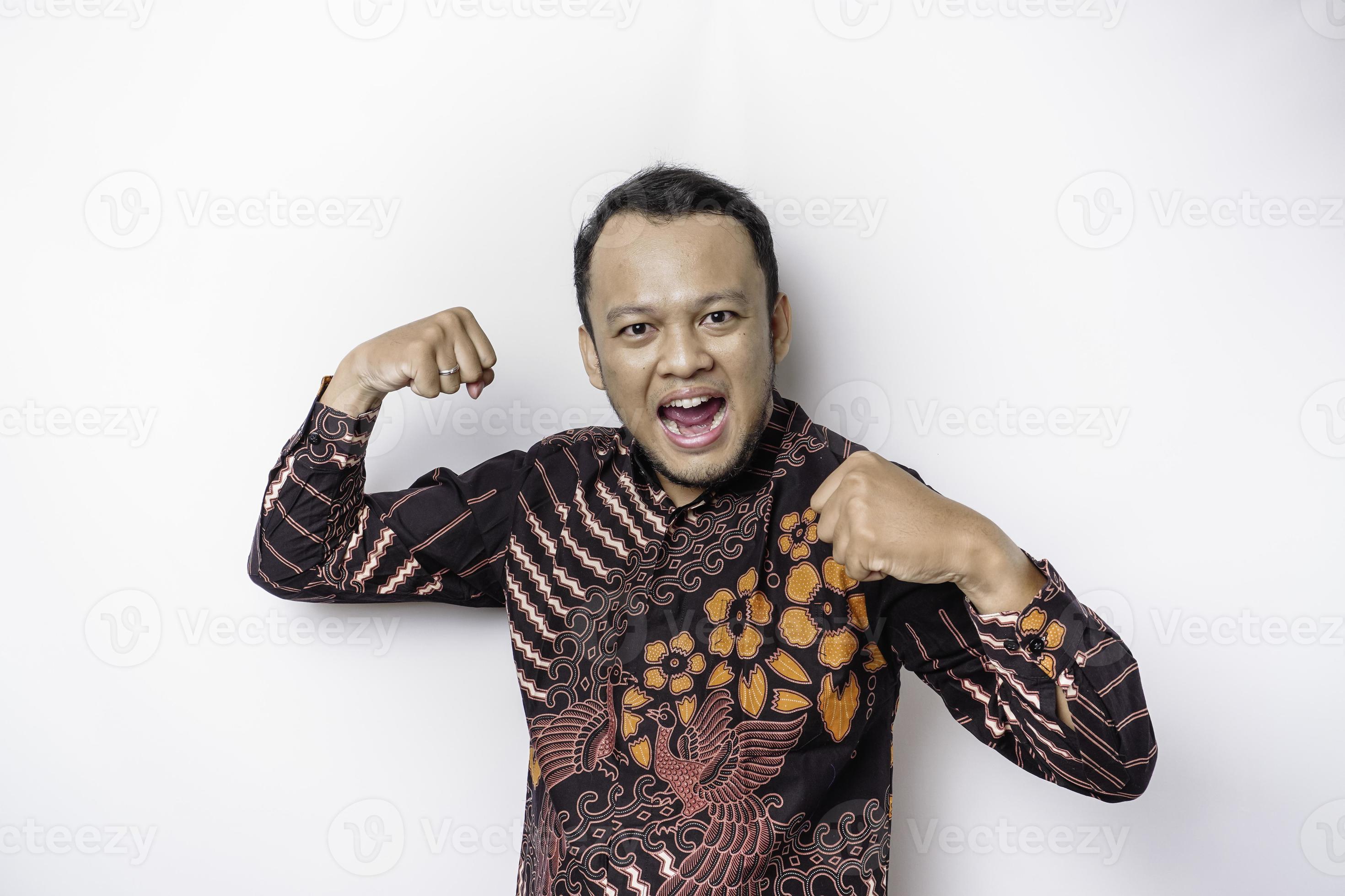 Excited Asian man wearing batik shirt showing strong gesture by lifting ...