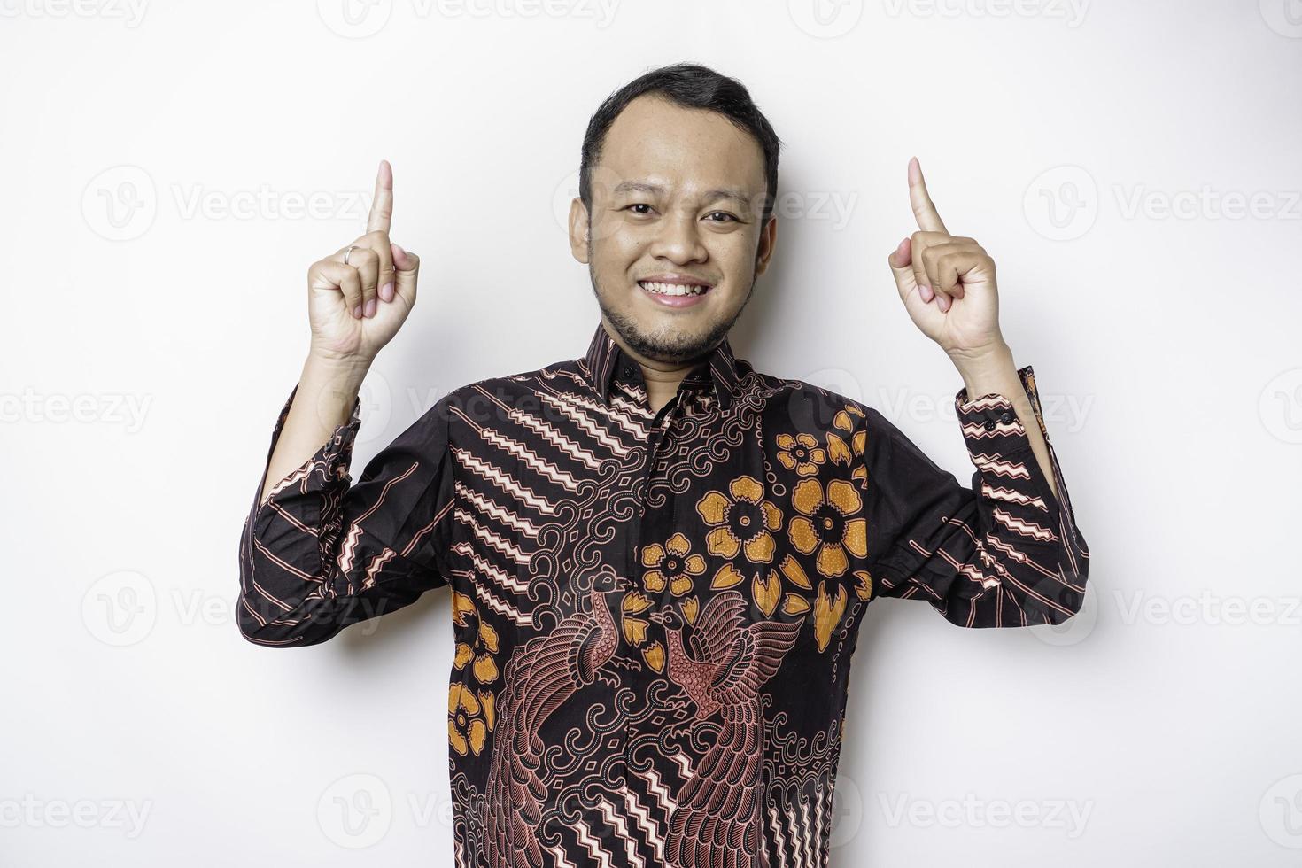 Excited Asian man wearing batik shirt pointing at the copy space on top ...