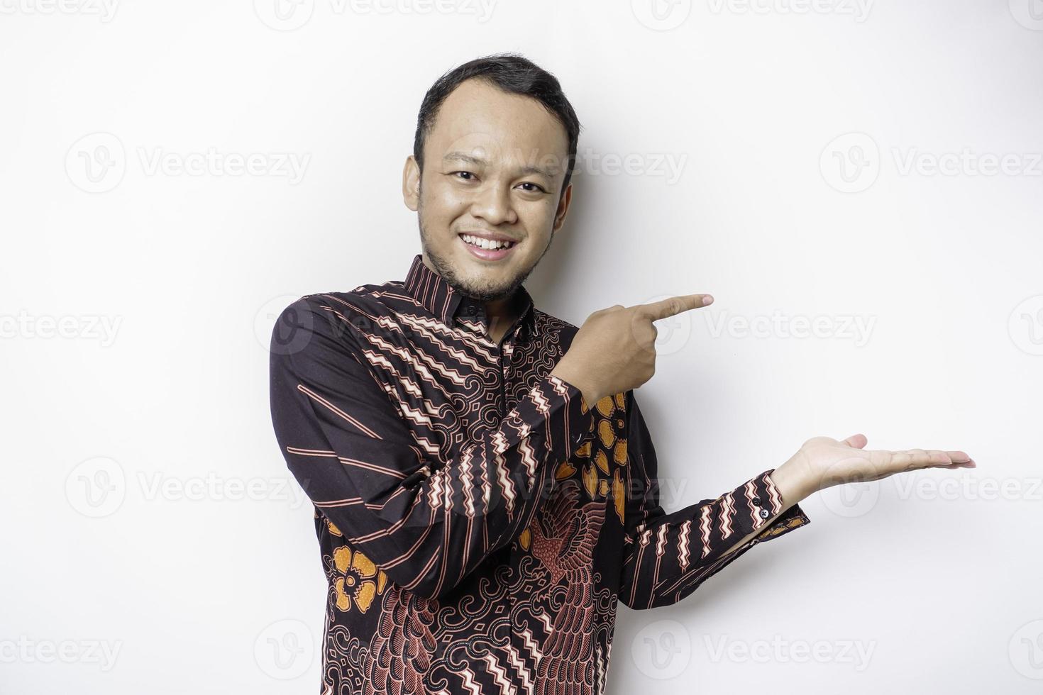 Excited Asian man wearing batik shirt pointing at the copy space beside ...