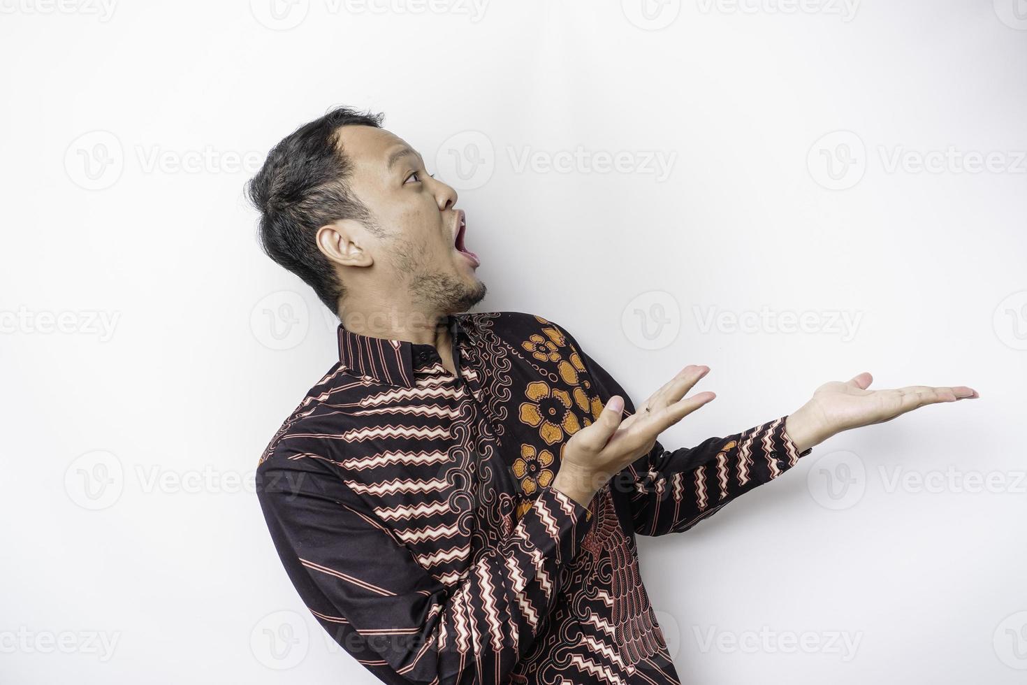 Shocked Asian man wearing batik shirt pointing at the copy space beside ...
