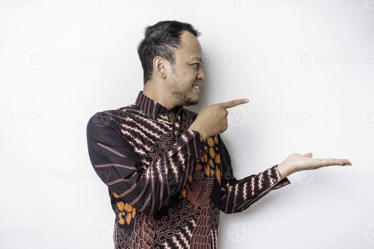 Excited Asian man wearing batik shirt pointing at the copy space beside ...