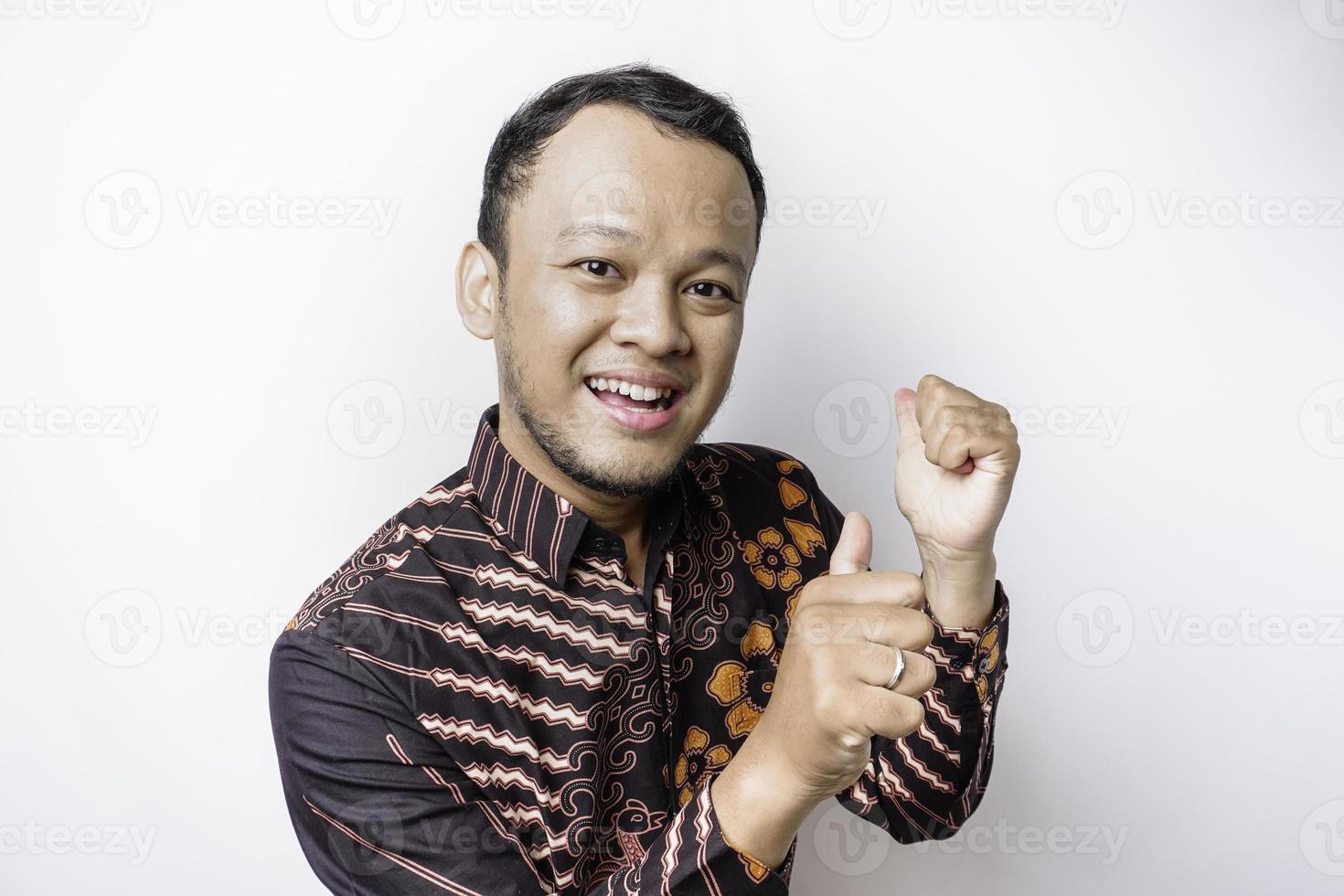 Excited Asian man wearing batik shirt pointing at the copy space on top ...