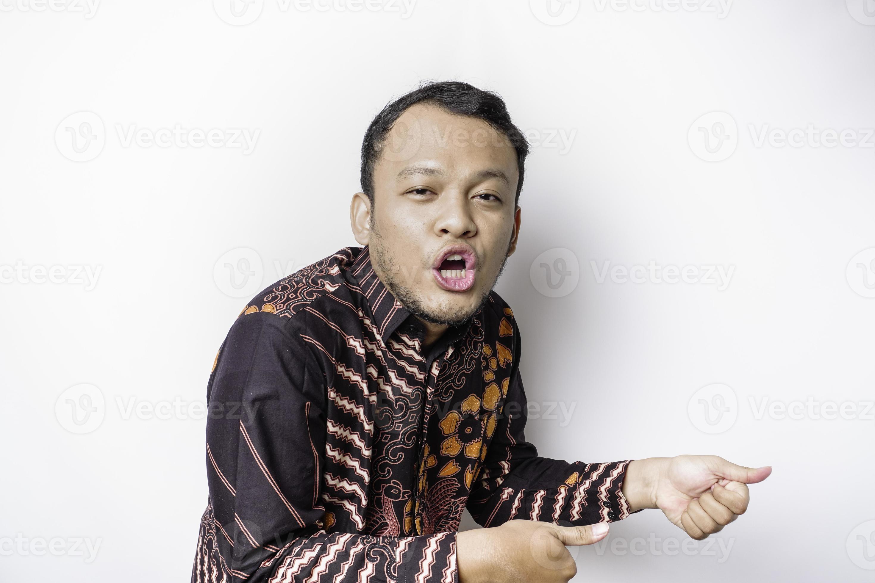Shocked Asian man wearing batik shirt pointing at the copy space beside ...