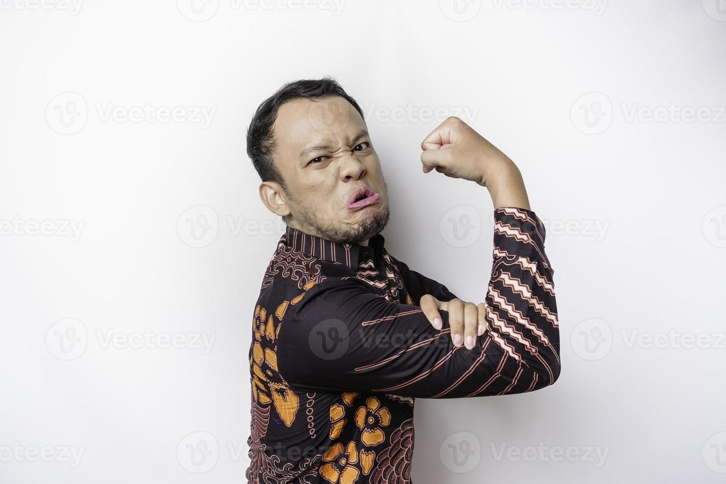 Excited Asian man wearing batik shirt showing strong gesture by lifting ...