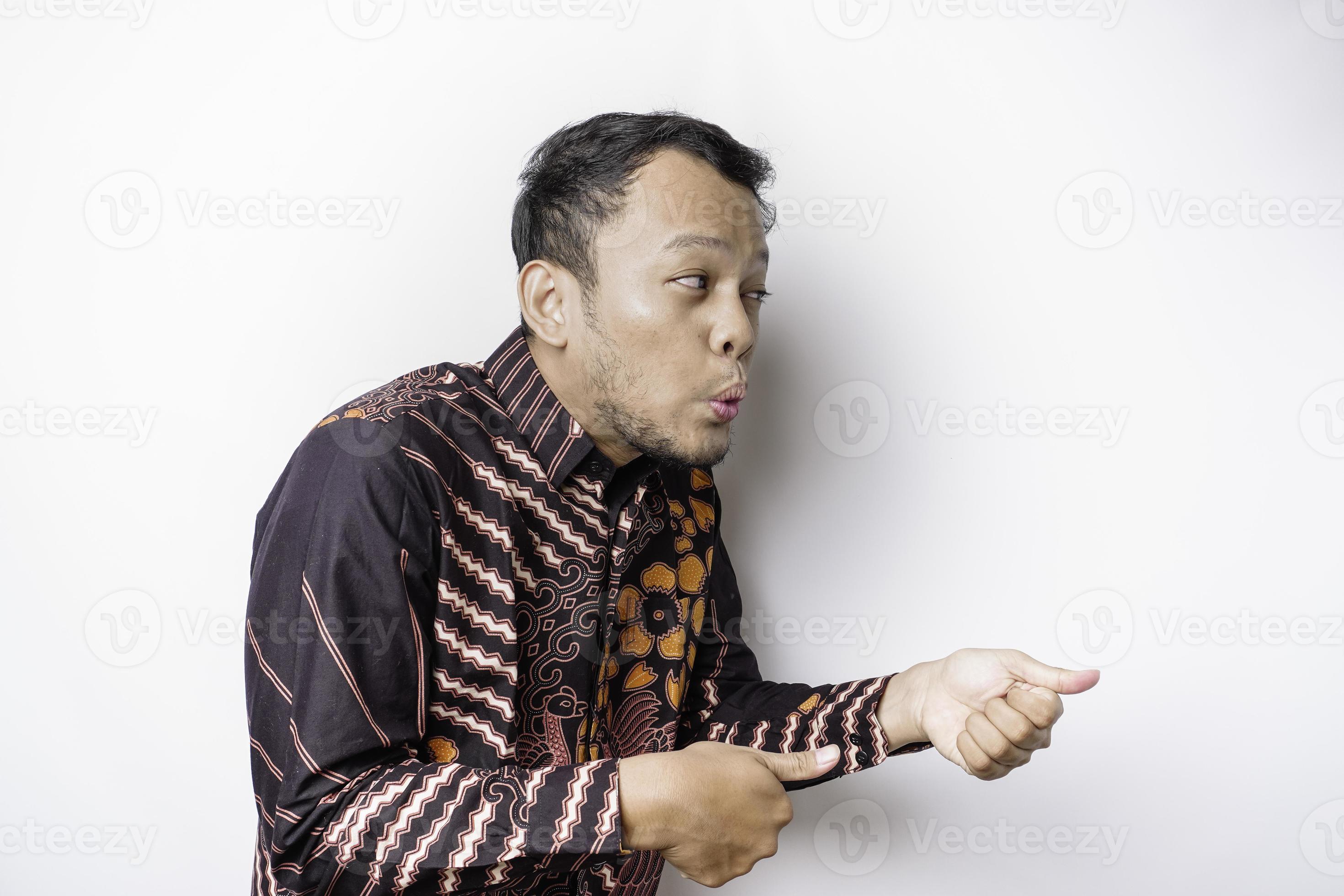 Shocked Asian man wearing batik shirt pointing at the copy space beside ...