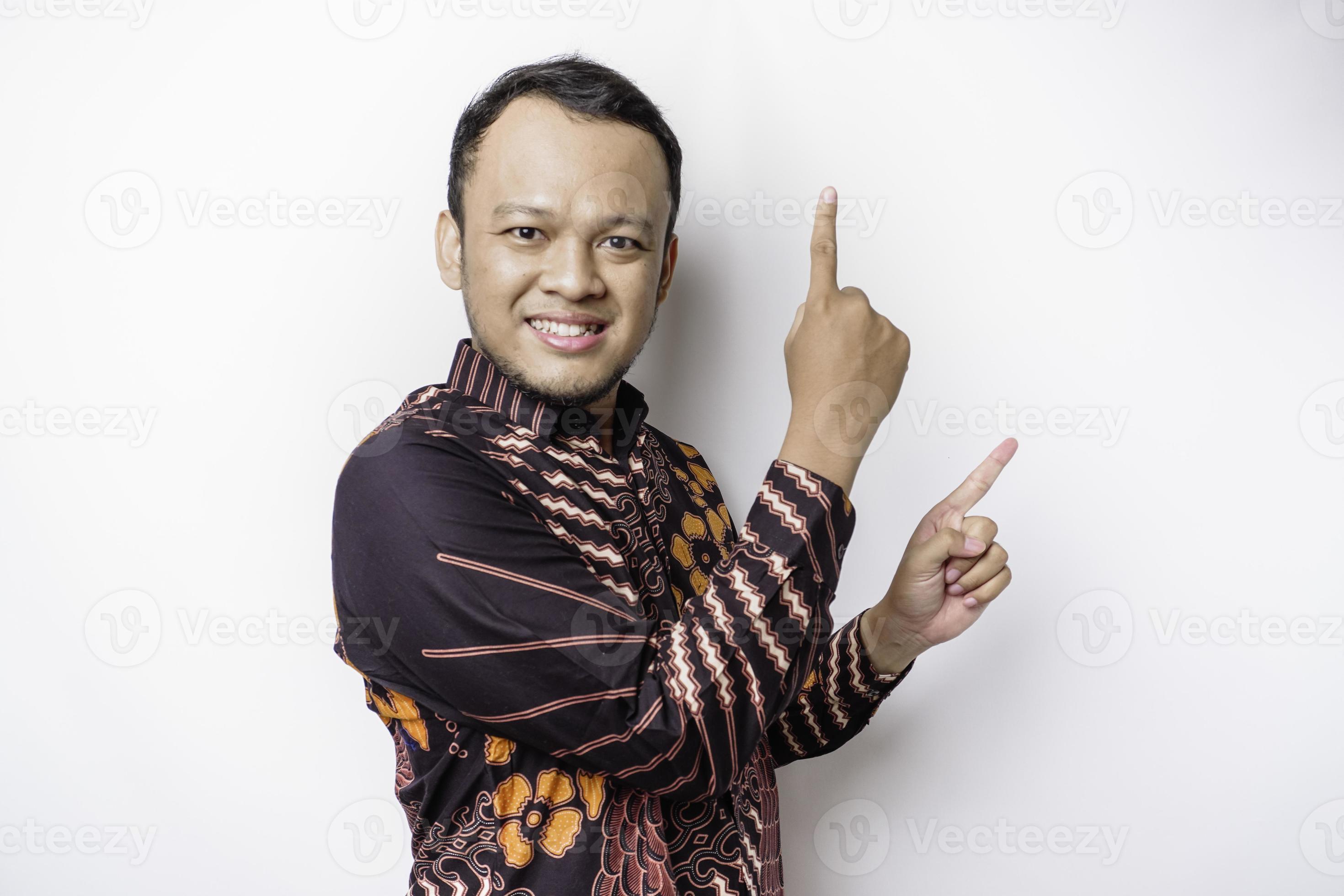Excited Asian man wearing batik shirt pointing at the copy space on top ...