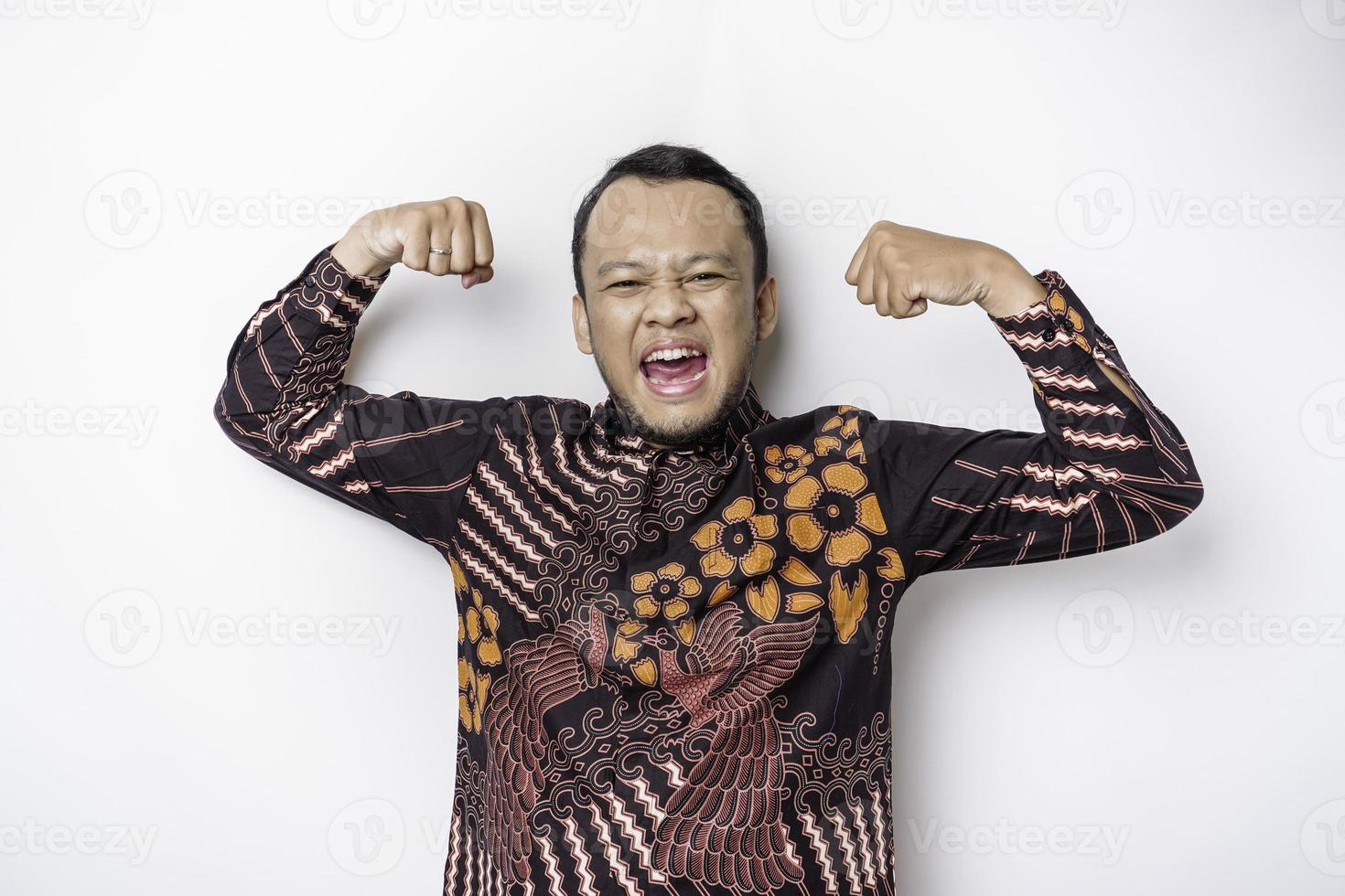 Excited Asian man wearing batik shirt showing strong gesture by lifting ...