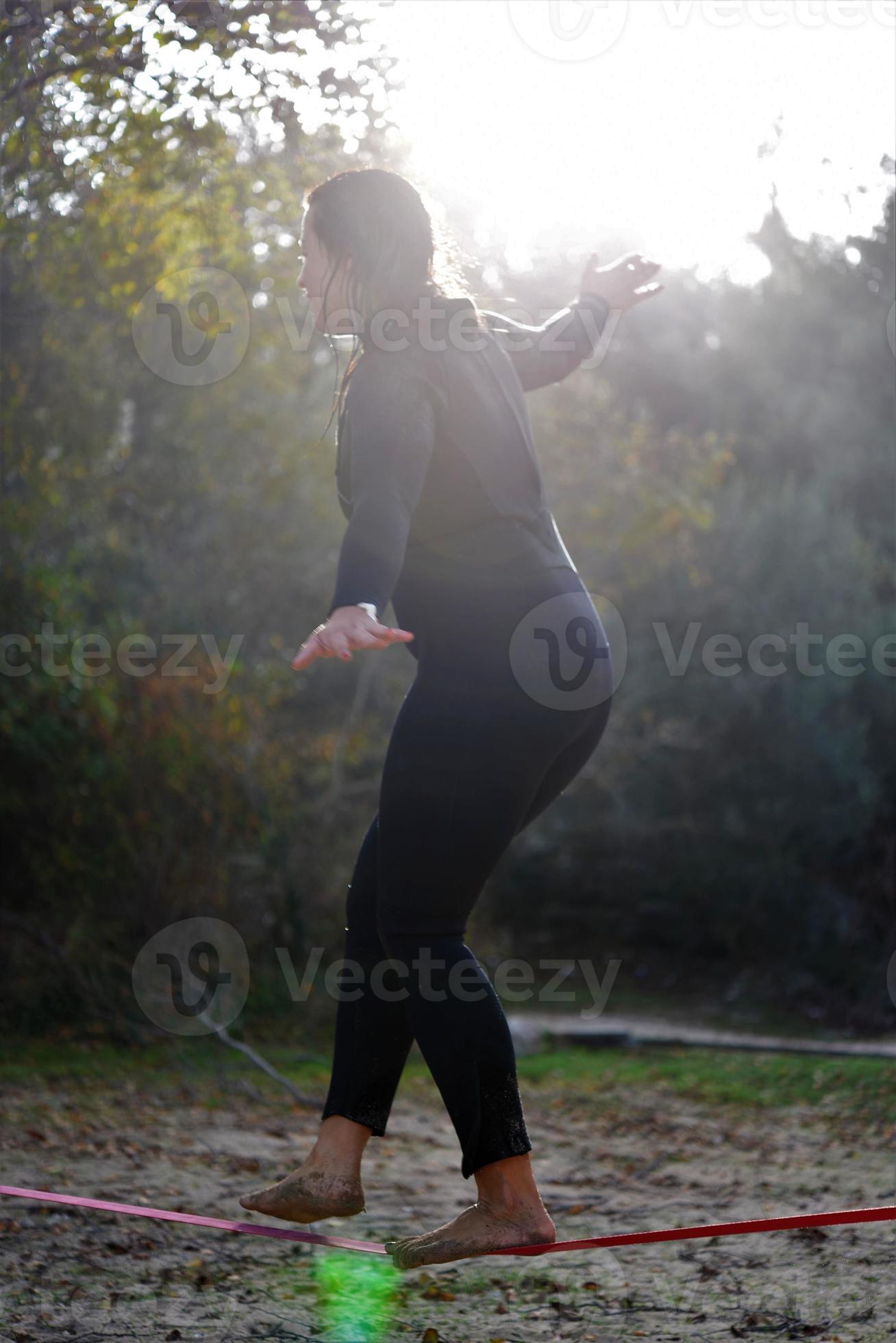 Woman balancing her walk on a loose rope tied between two trees. Woman practicing slack rope ...
