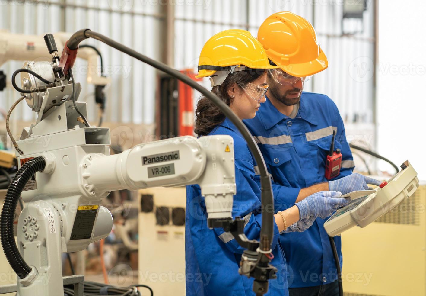 Male Industrial Engineer Using Remote Control Board To Check Robotic Welder Operation In Modern