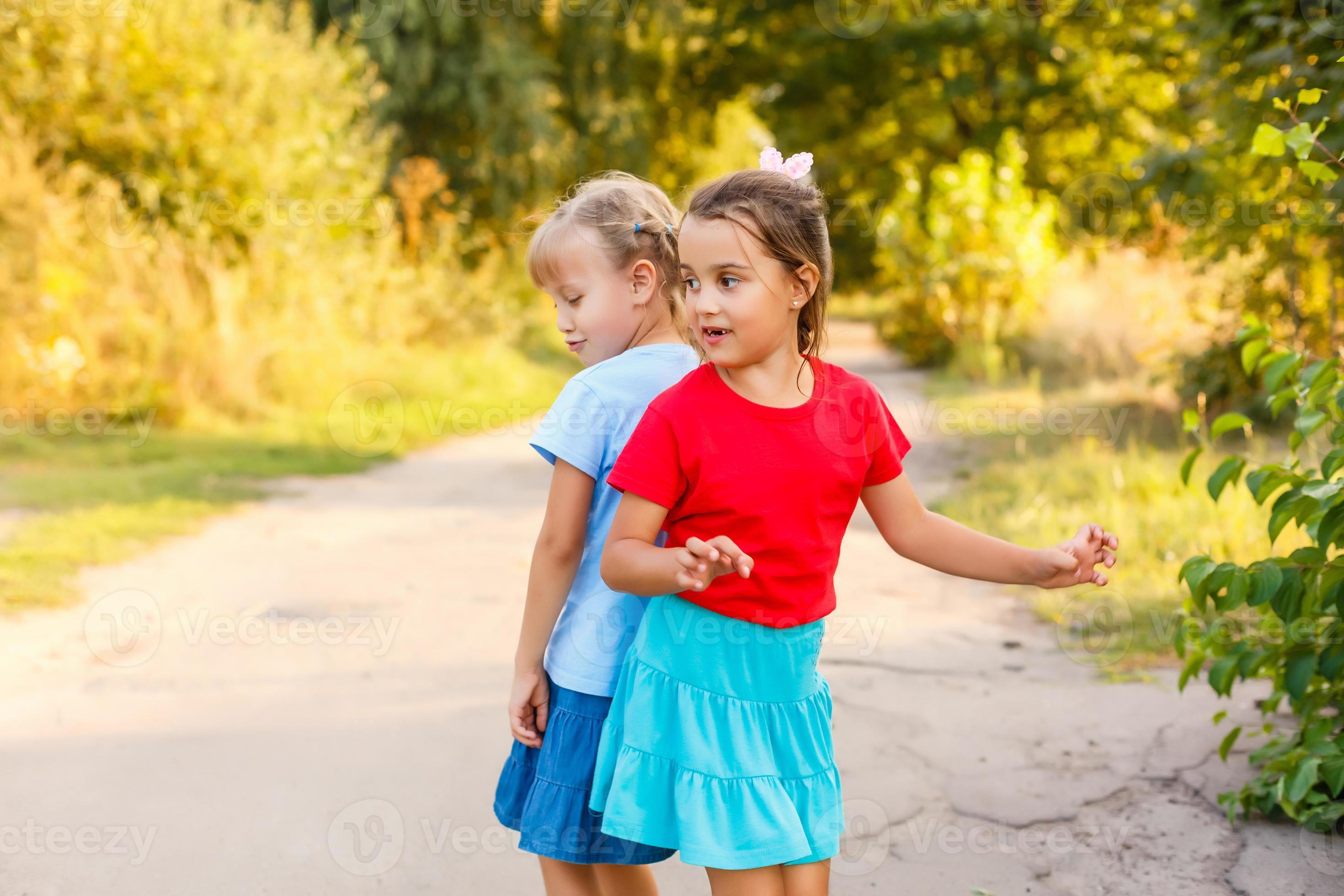 Back view of two little girls holding hand and walking together in the garden in vintage color ...