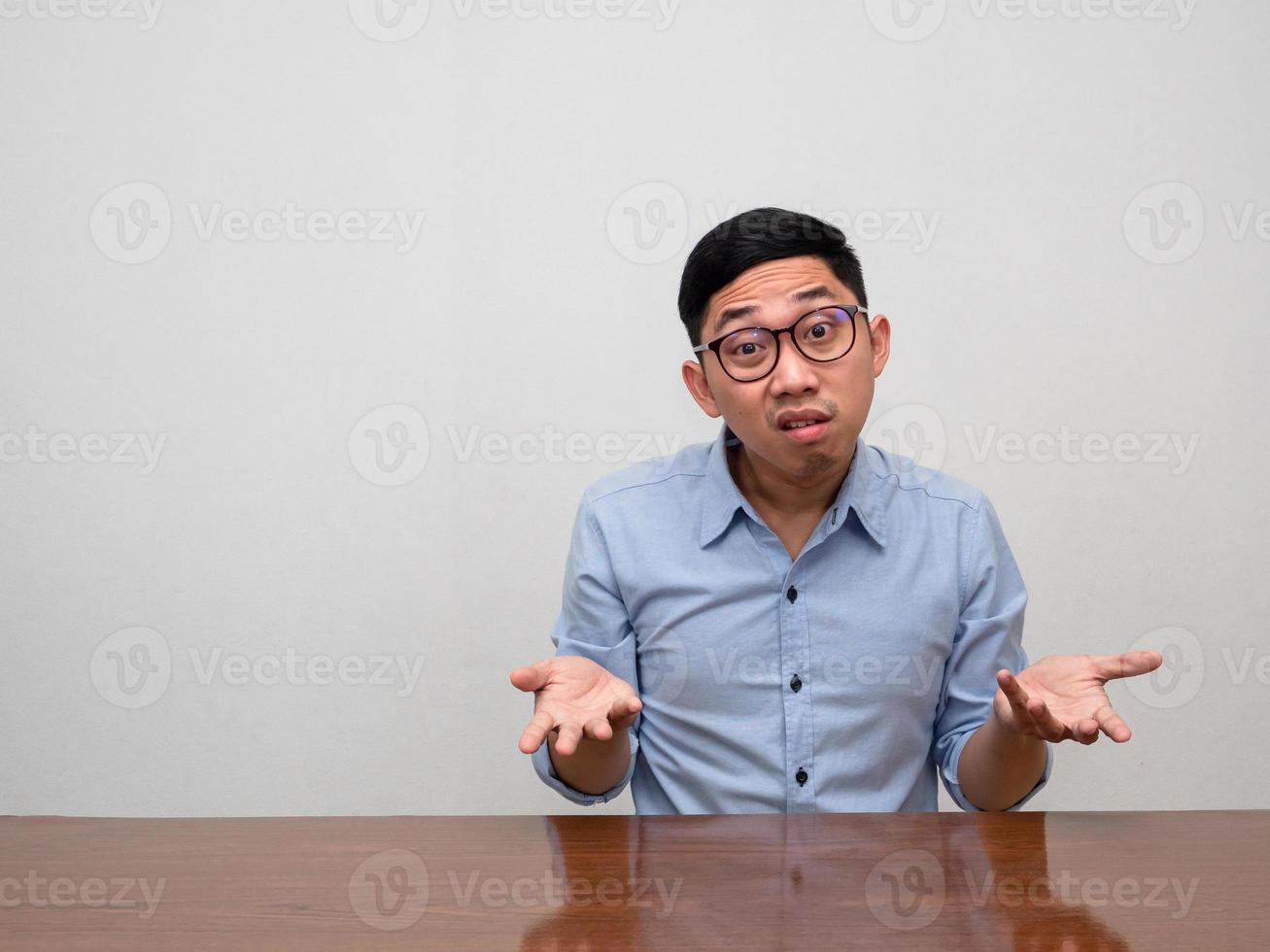 Asian Businessman Wear Glasses Sit At Table Gesture Confused And Doubt