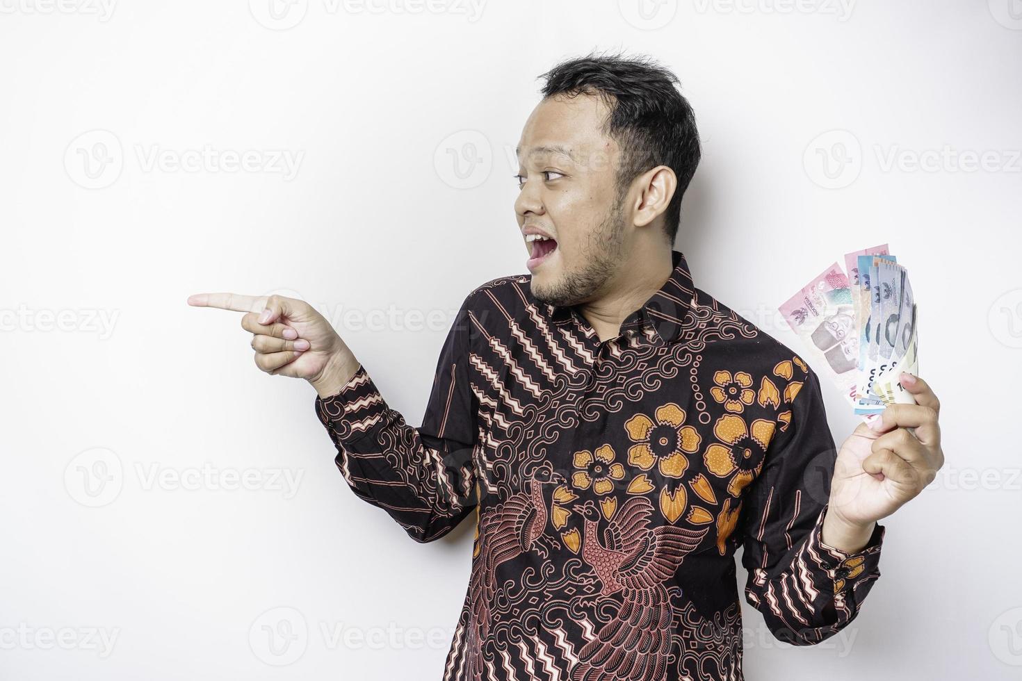 A happy young Asian man is wearing batik shirt, pointing at the copy ...