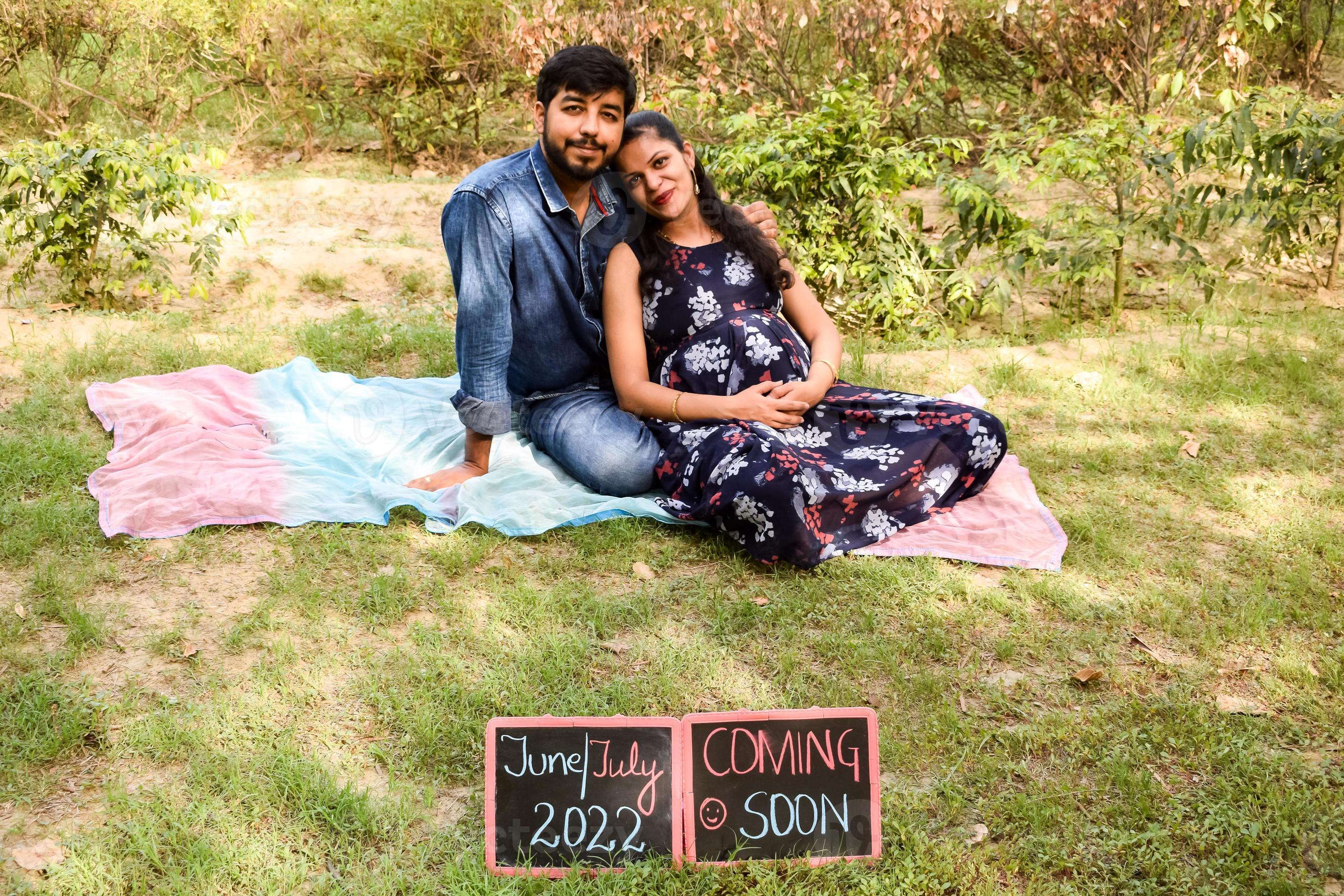 pareja india posando para una sesión de fotos de maternidad. la pareja está posando en un césped ...