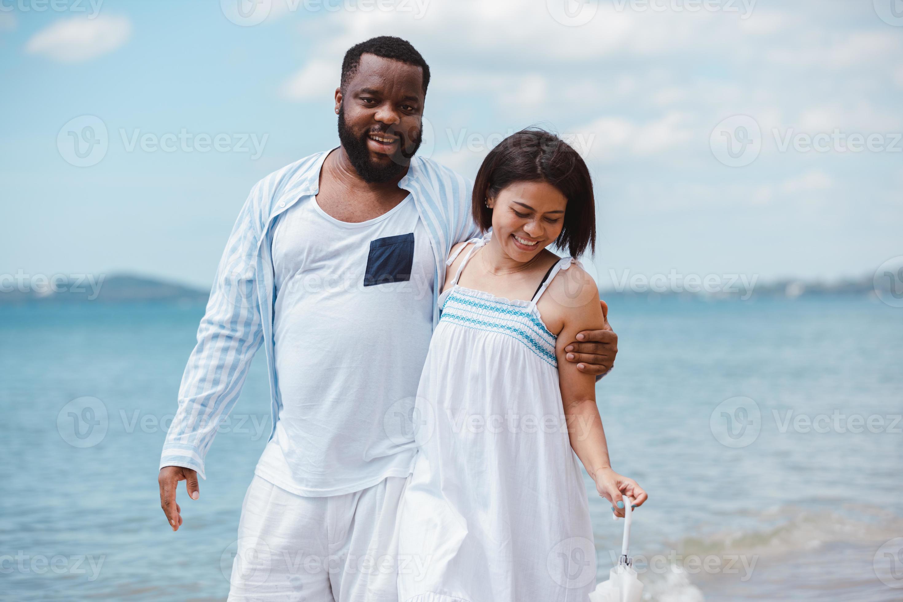 Happy American African couple laughing and having fun together while walking on the beach ...