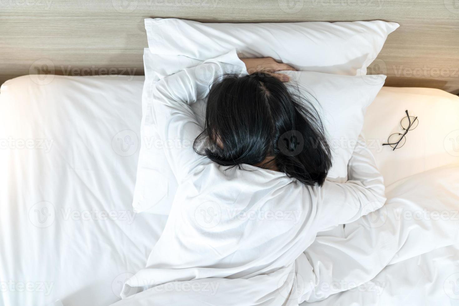 Asian Lady in white long arm t-shirt pajamas lie prone, lie on the stomach in bed with tried and ...