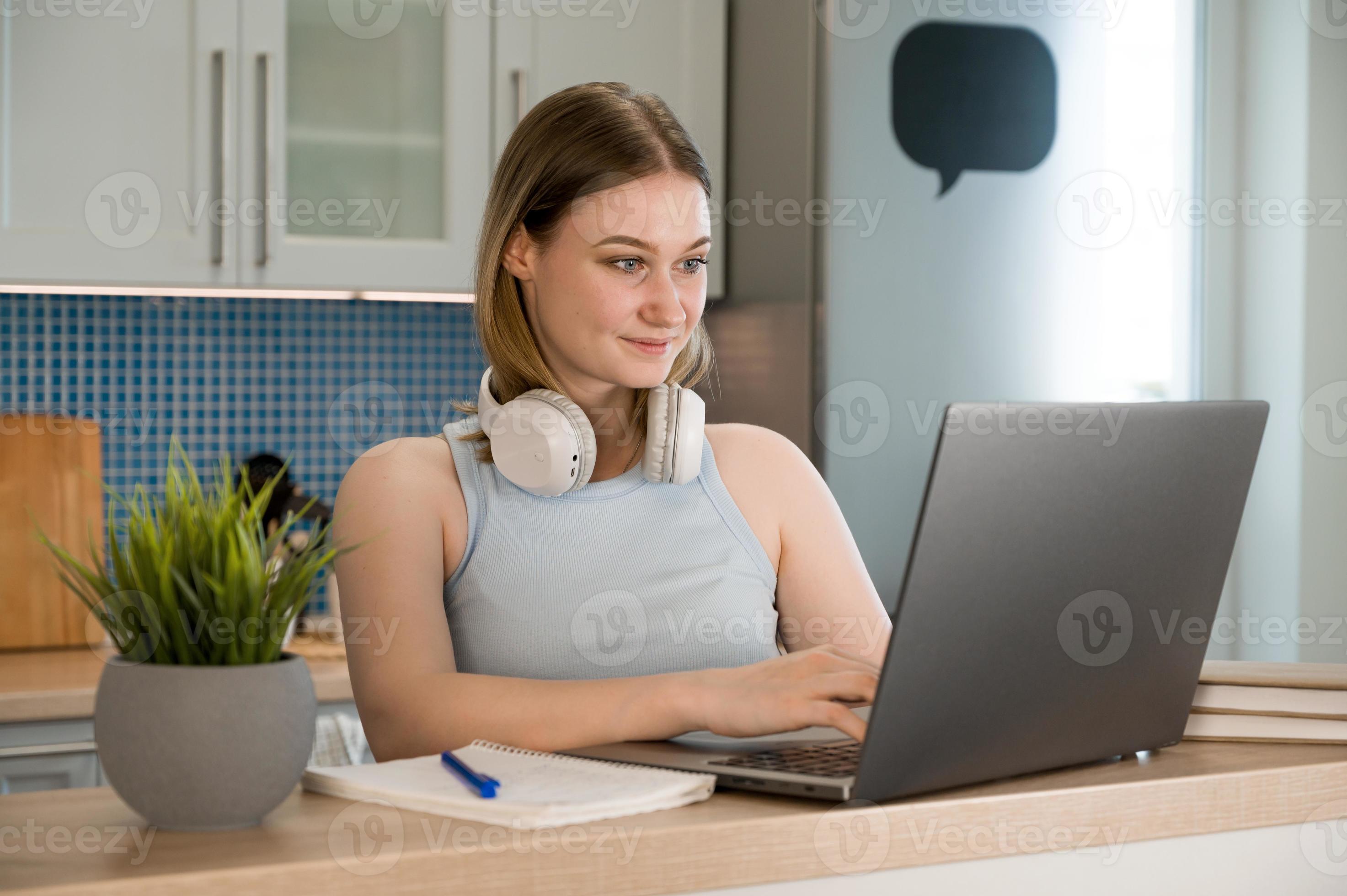 mujer joven feliz trabajando en una computadora portátil en la cocina. estudiante escribiendo ...