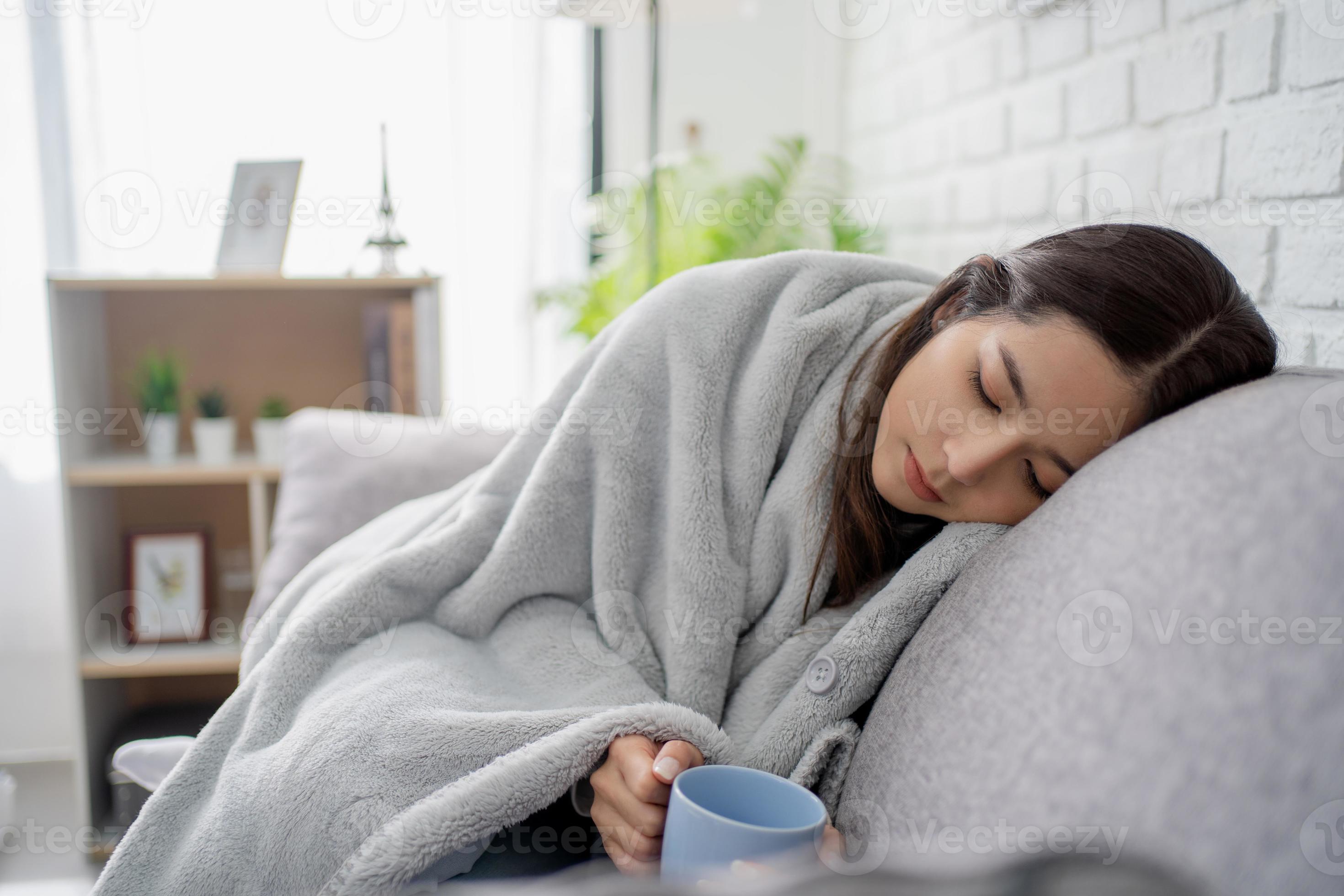 Feeling sick. Sick young women covered with blanket resting at home while sitting on the sofa ...