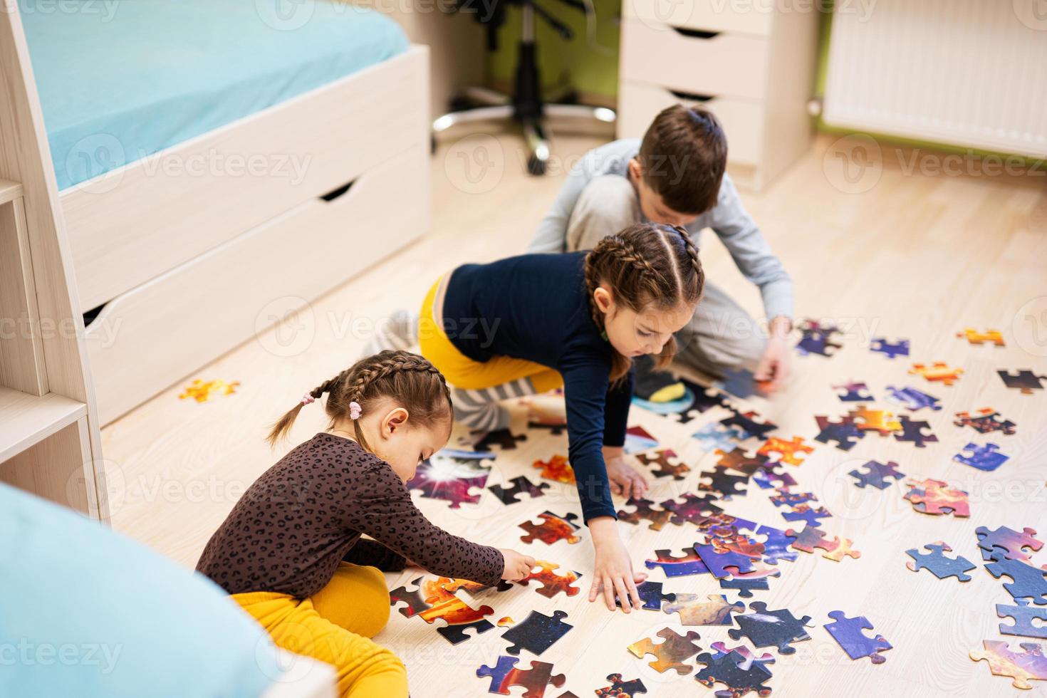 Children connecting jigsaw puzzle pieces in a kids room on floor at ...
