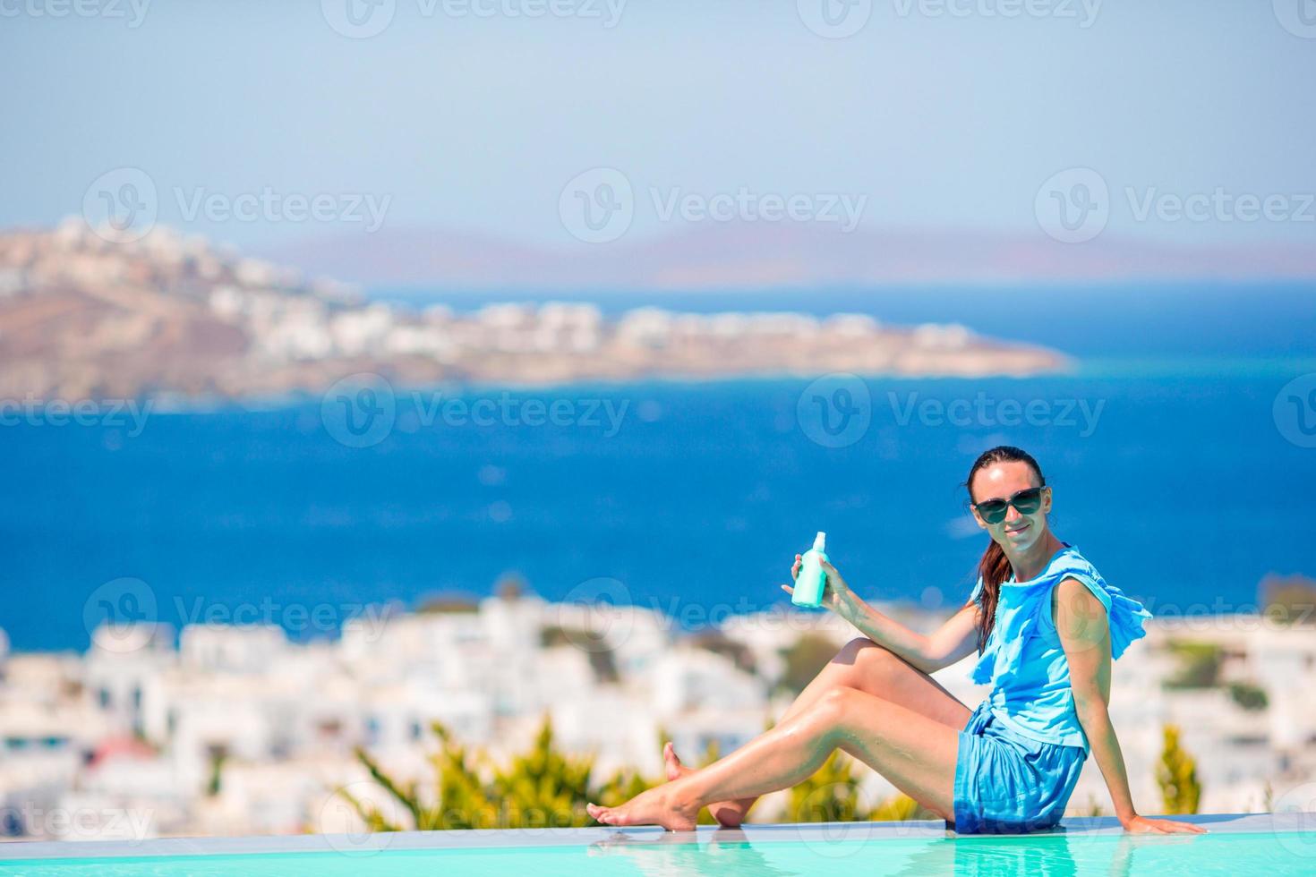 Young Woman Applying Sunscreen On Her Legs Sitting On The Edge Of Pool